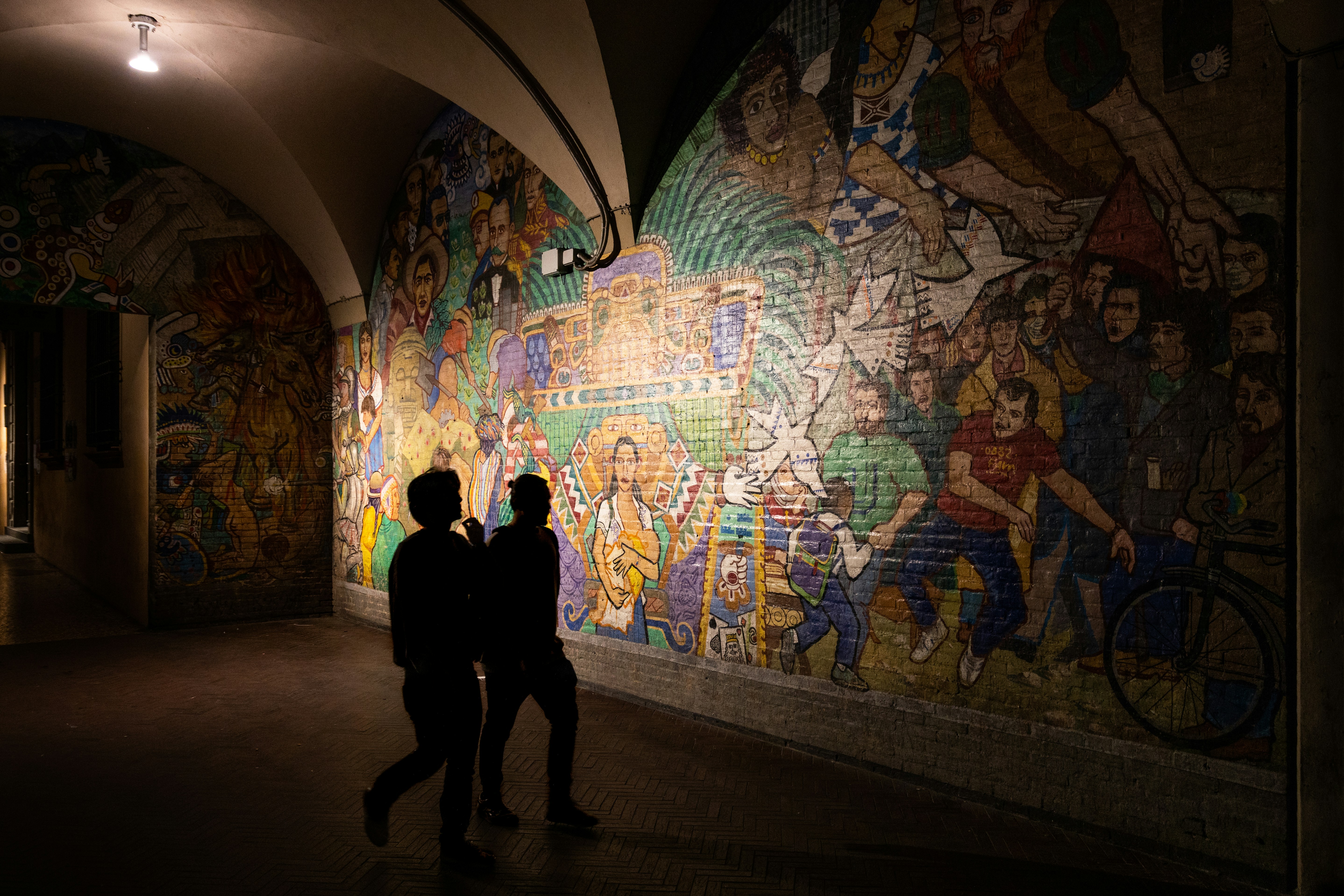 Shadowed Trio in a Muraled Tunnel