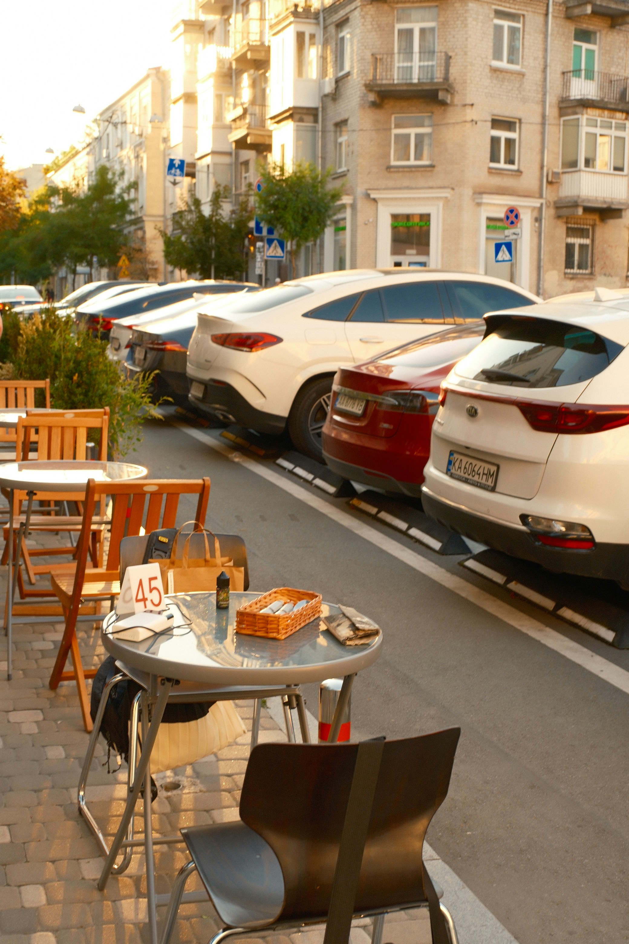 Evening Café Scene: Sunlit Street with Parked Cars and Outdoor Seating