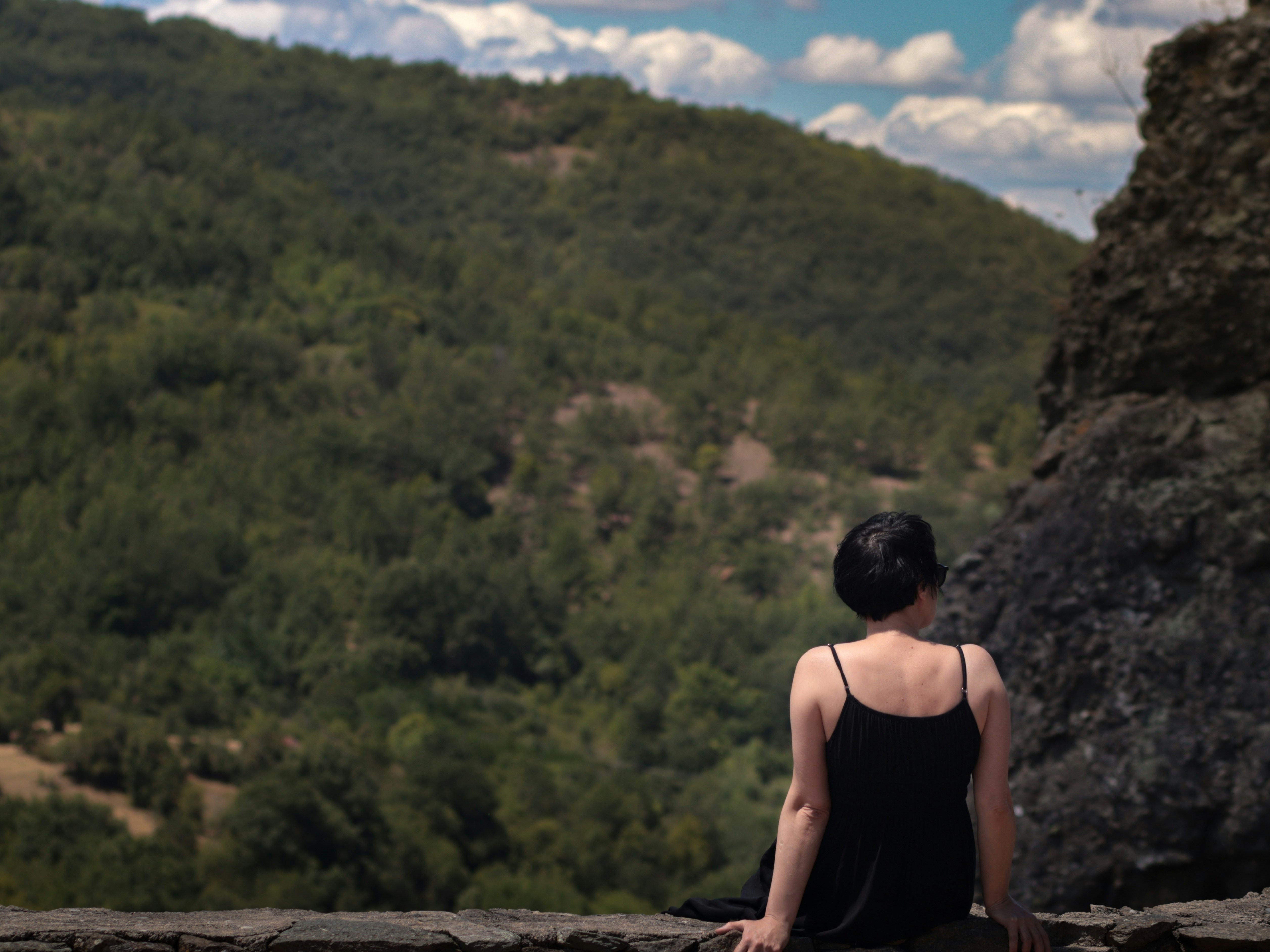 Edge of Solitude: A Woman in a Black Tank Top on a Cliff Overlooking Forested Valleys