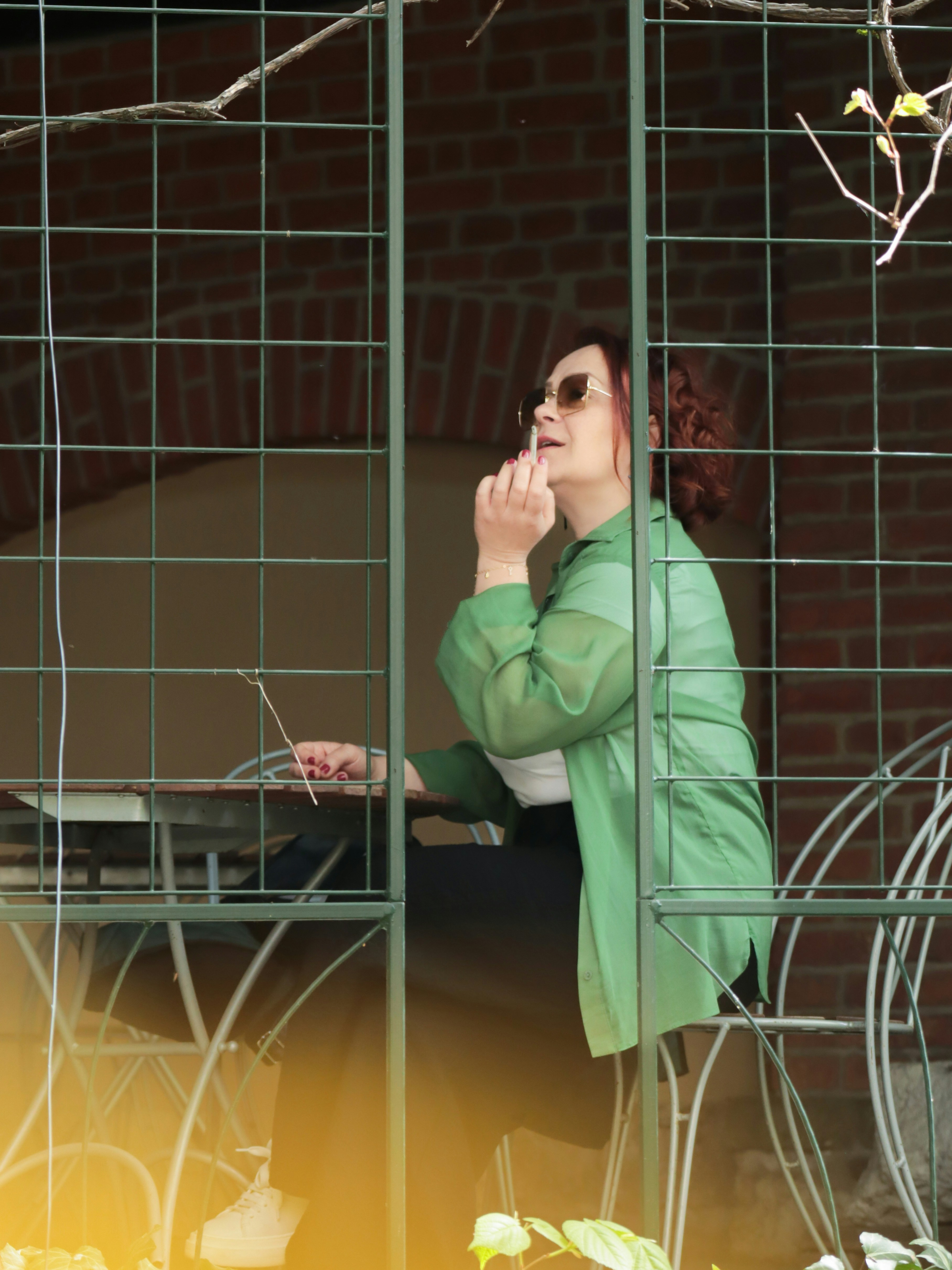 Green jacket, sunlit courtyard, and a pensive moment framed by iron lattice