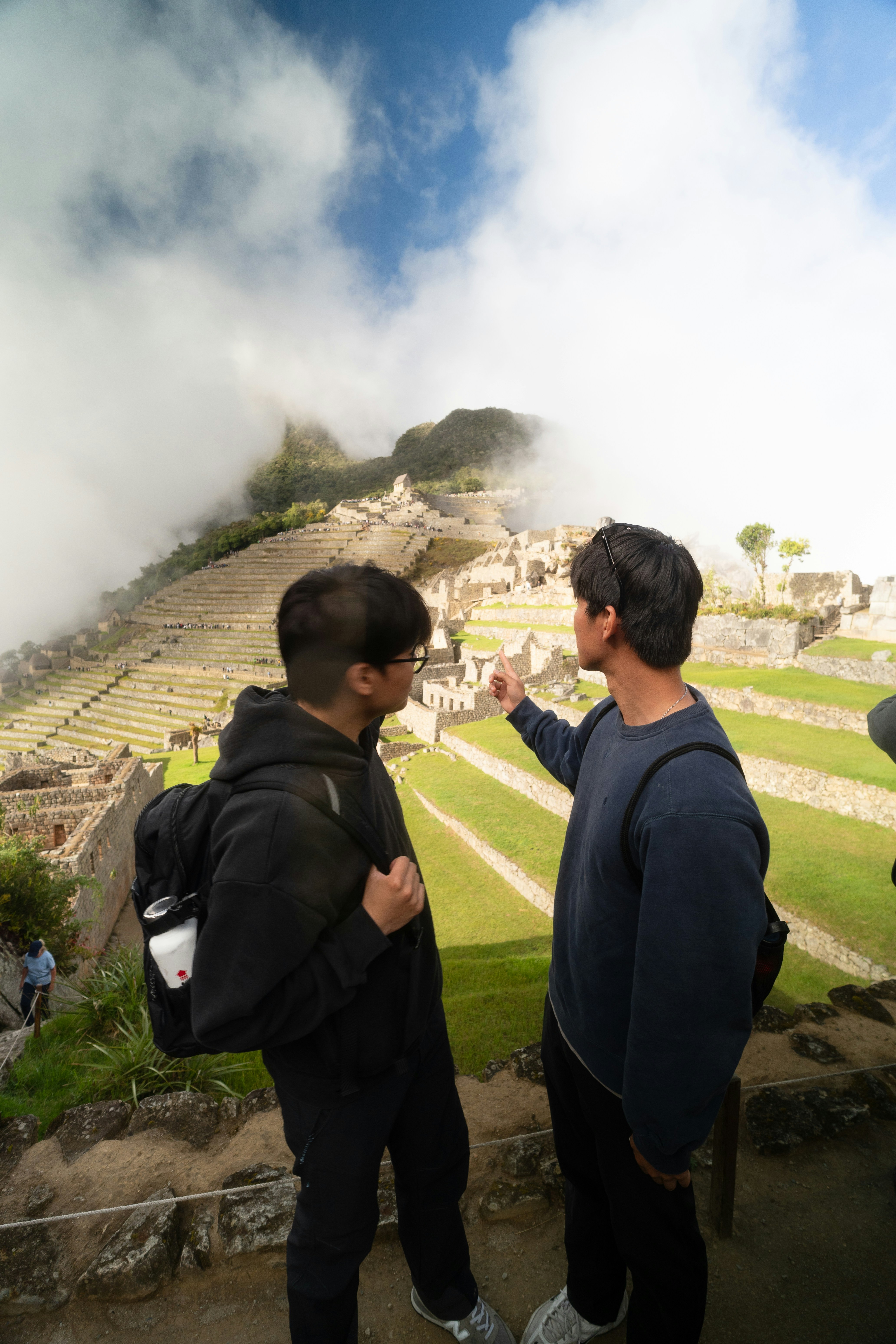Two hikers pause to admire ancient terraces under a cloud-kissed sky