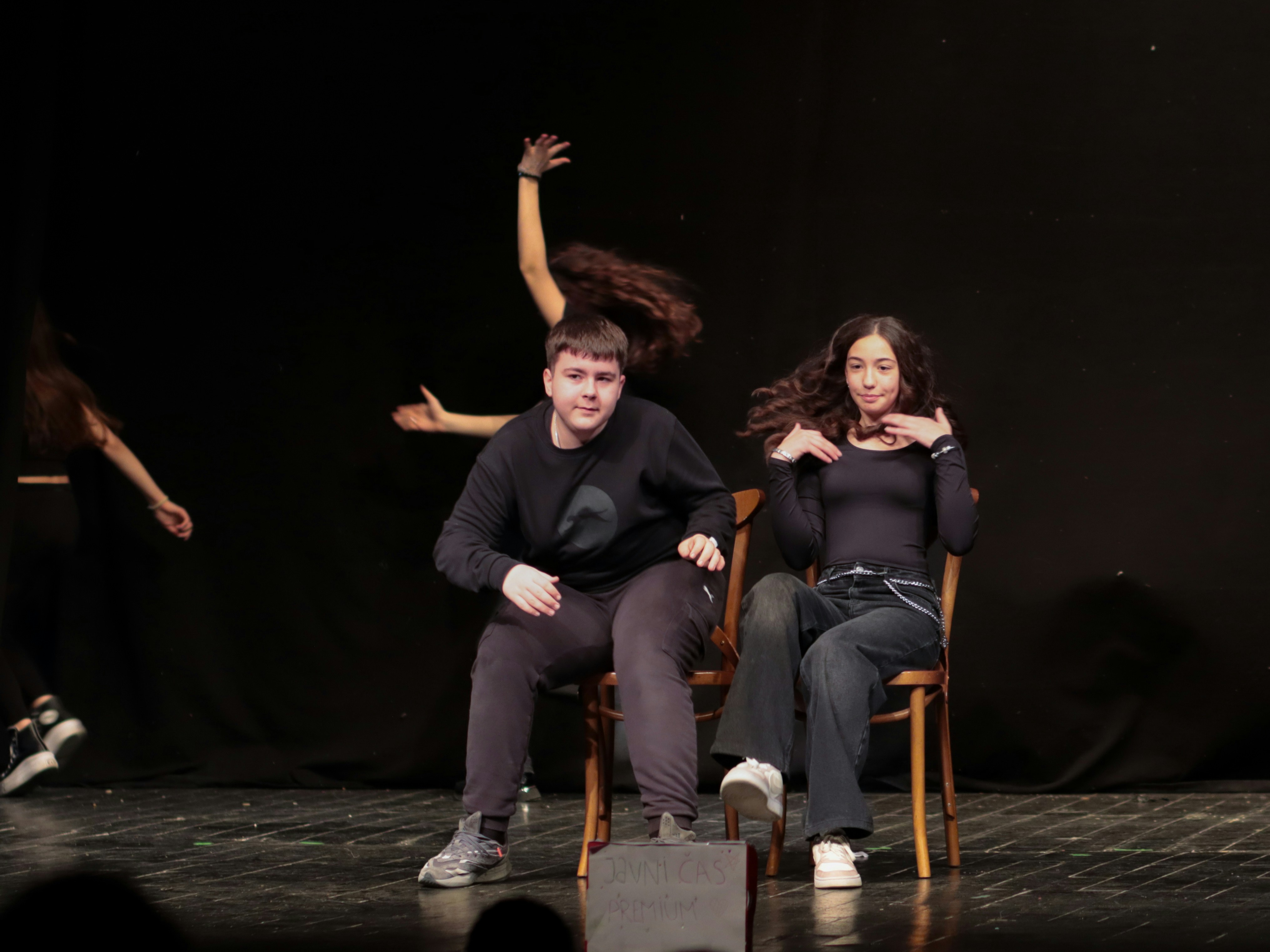 Two seated performers mid-action under stage lights