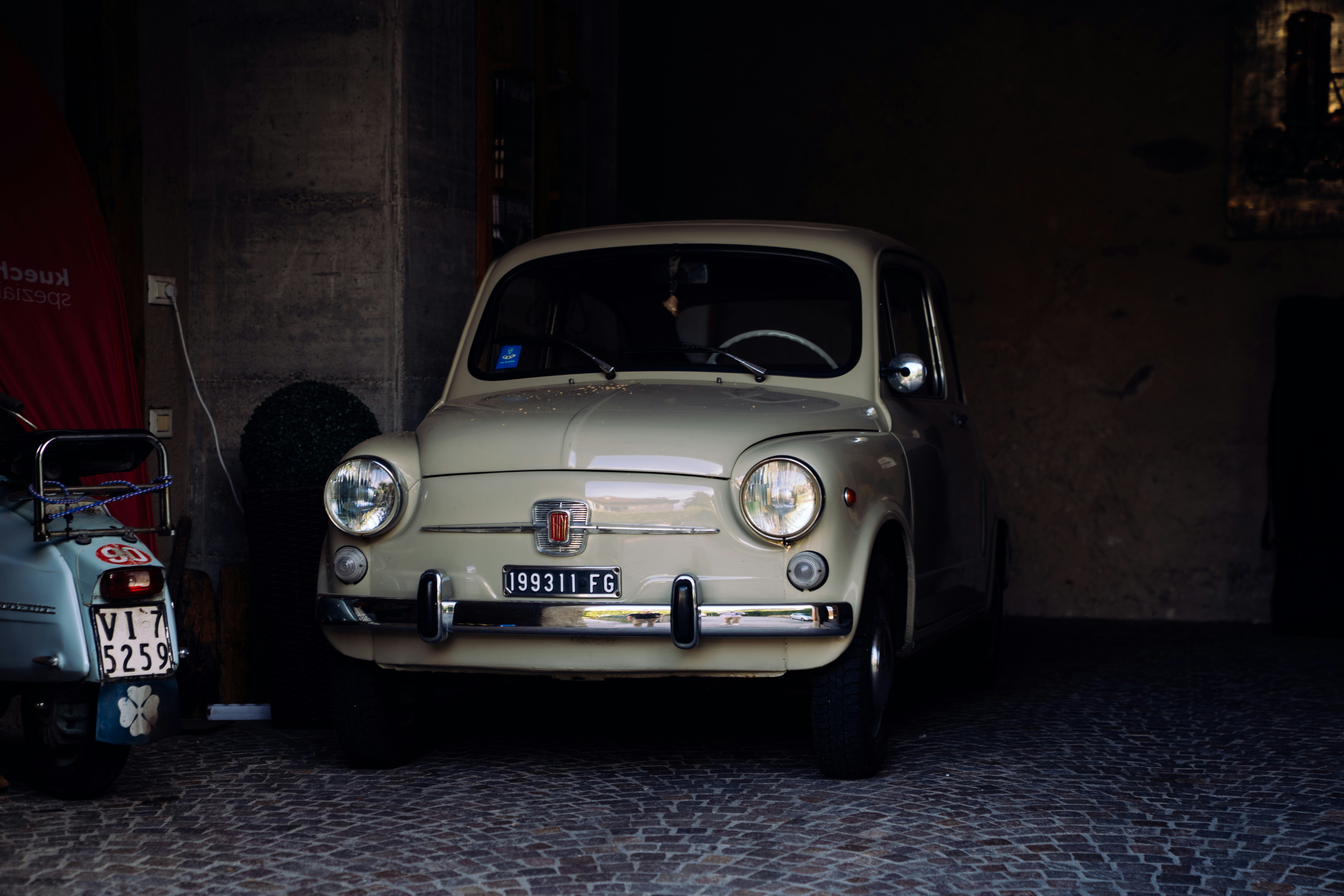 A vintage cream-colored Fiat 600 parked on a cobblestone surface.