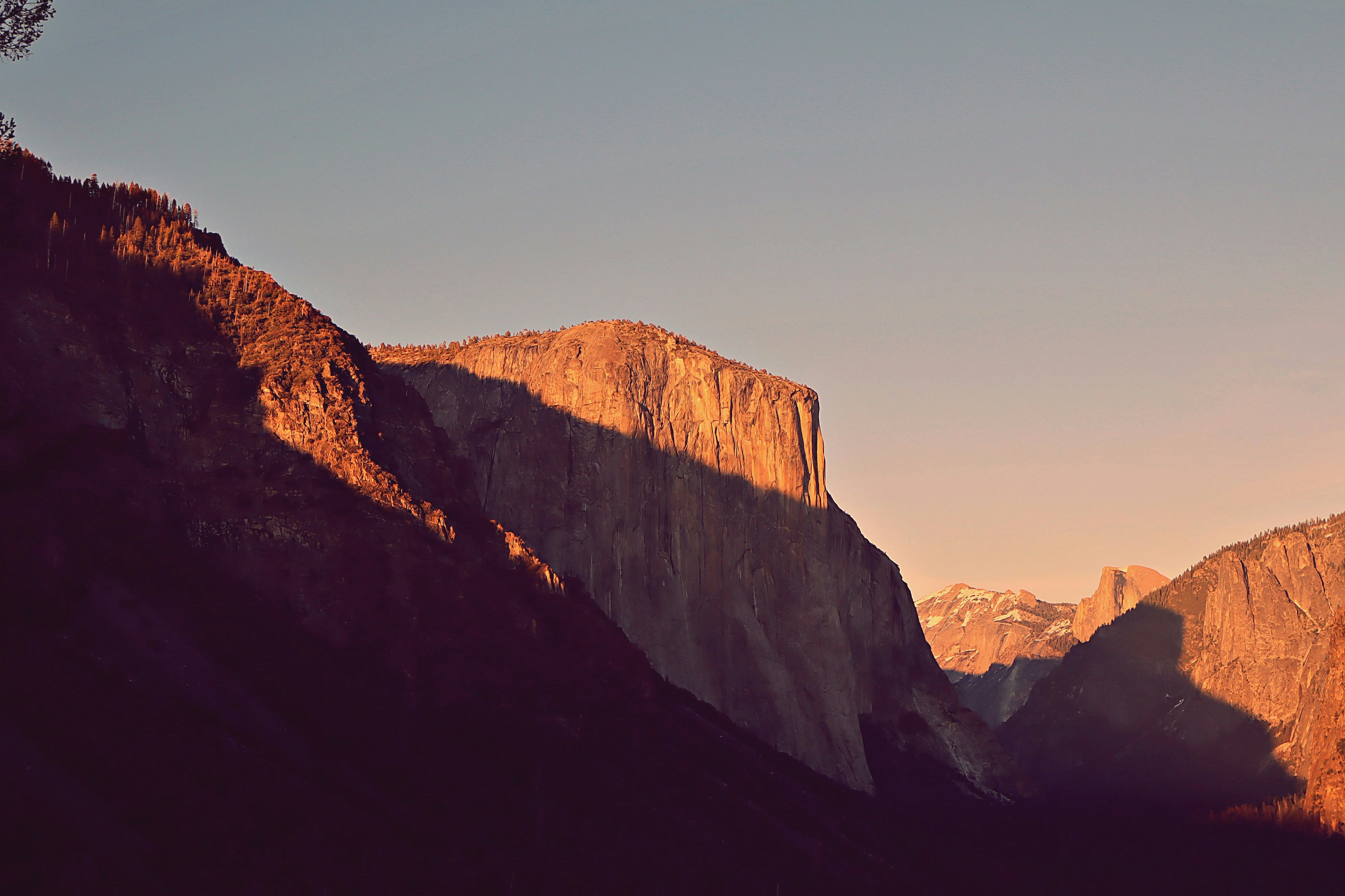 Dramatic mountain crest bathed in warm sunset light rises above shadowed valley walls.