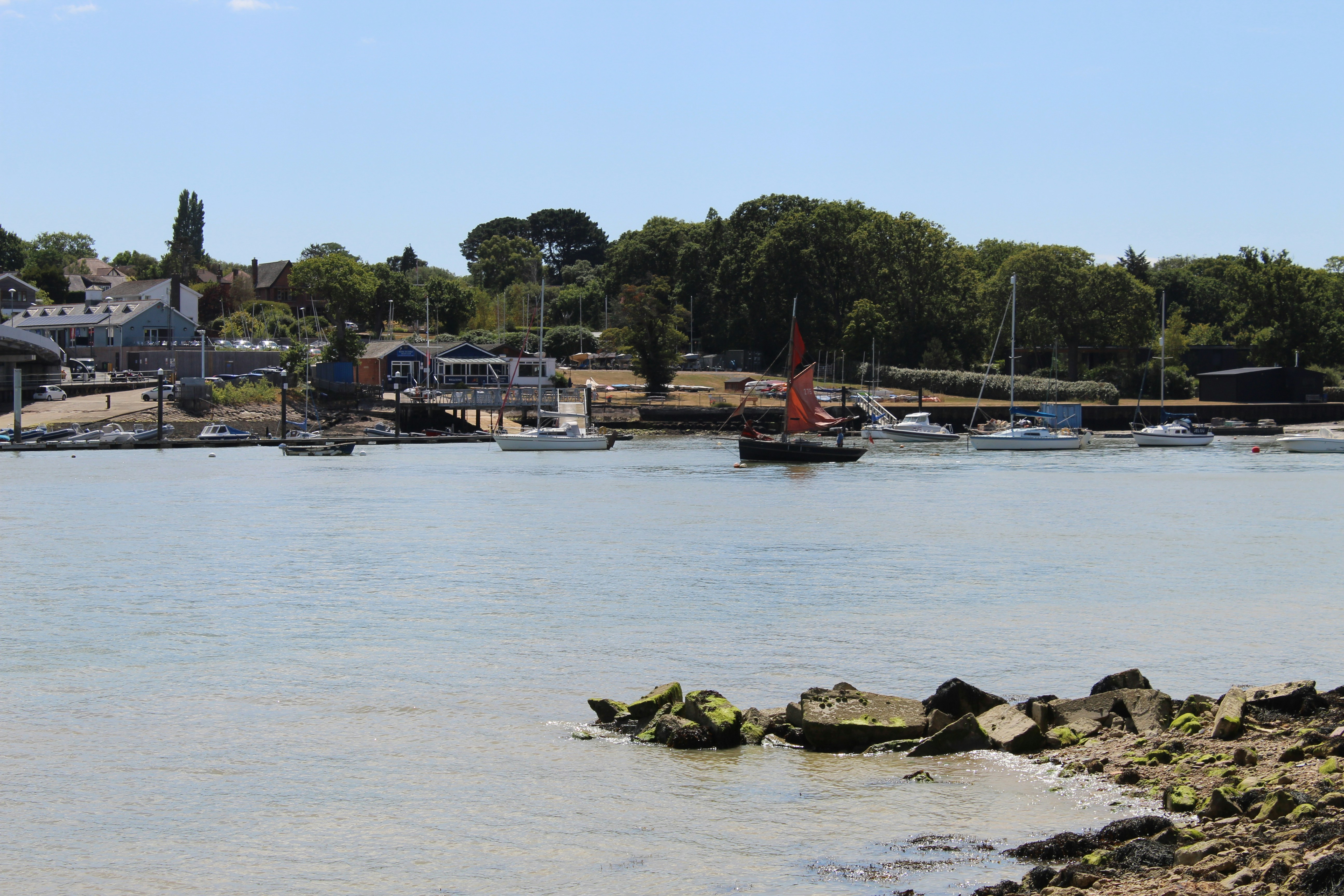Red-sailed boat at a calm harbor framed by cottages