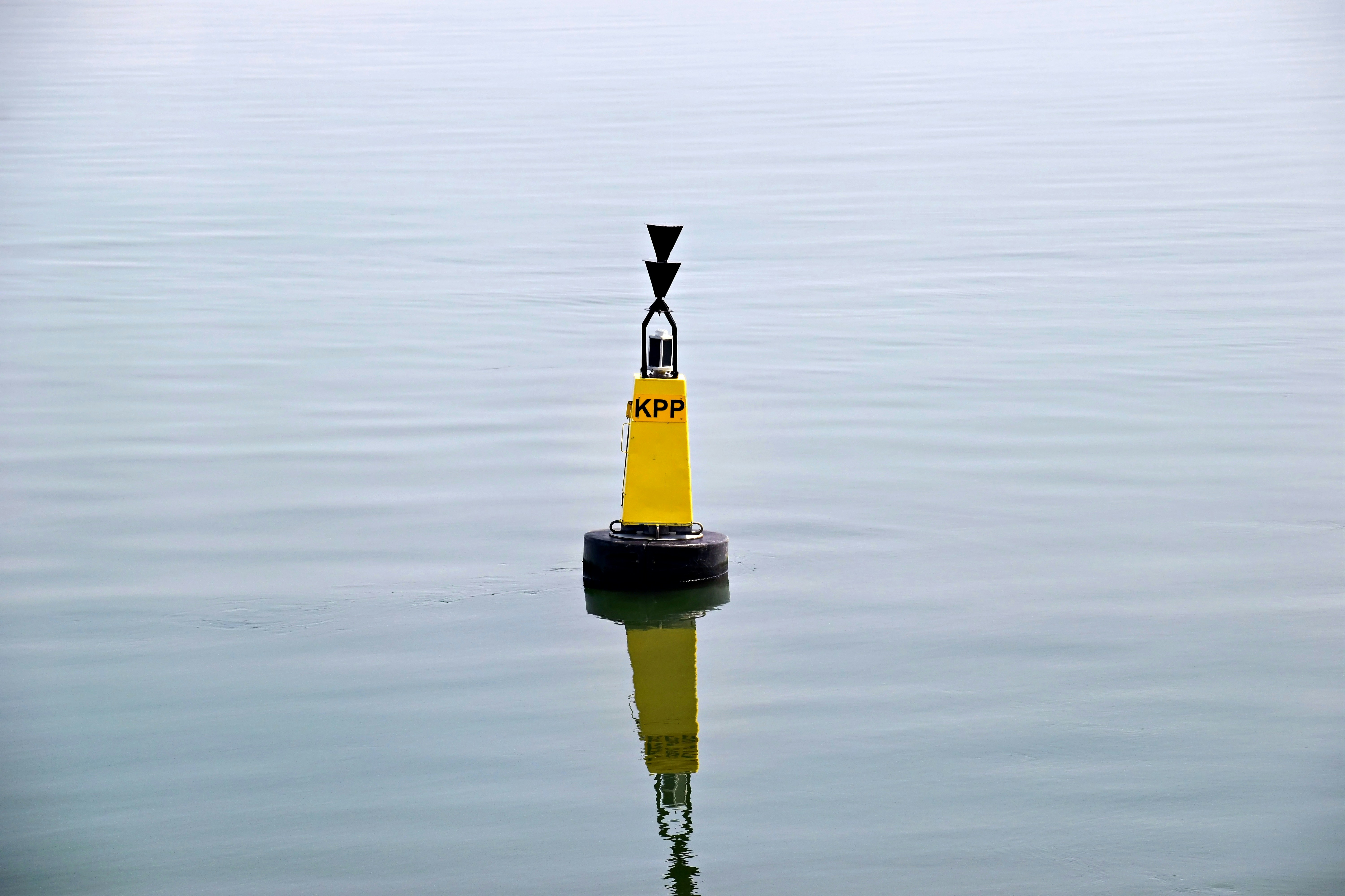 Yellow Beacon in Serene Blue: A solitary buoy with mirrored calm