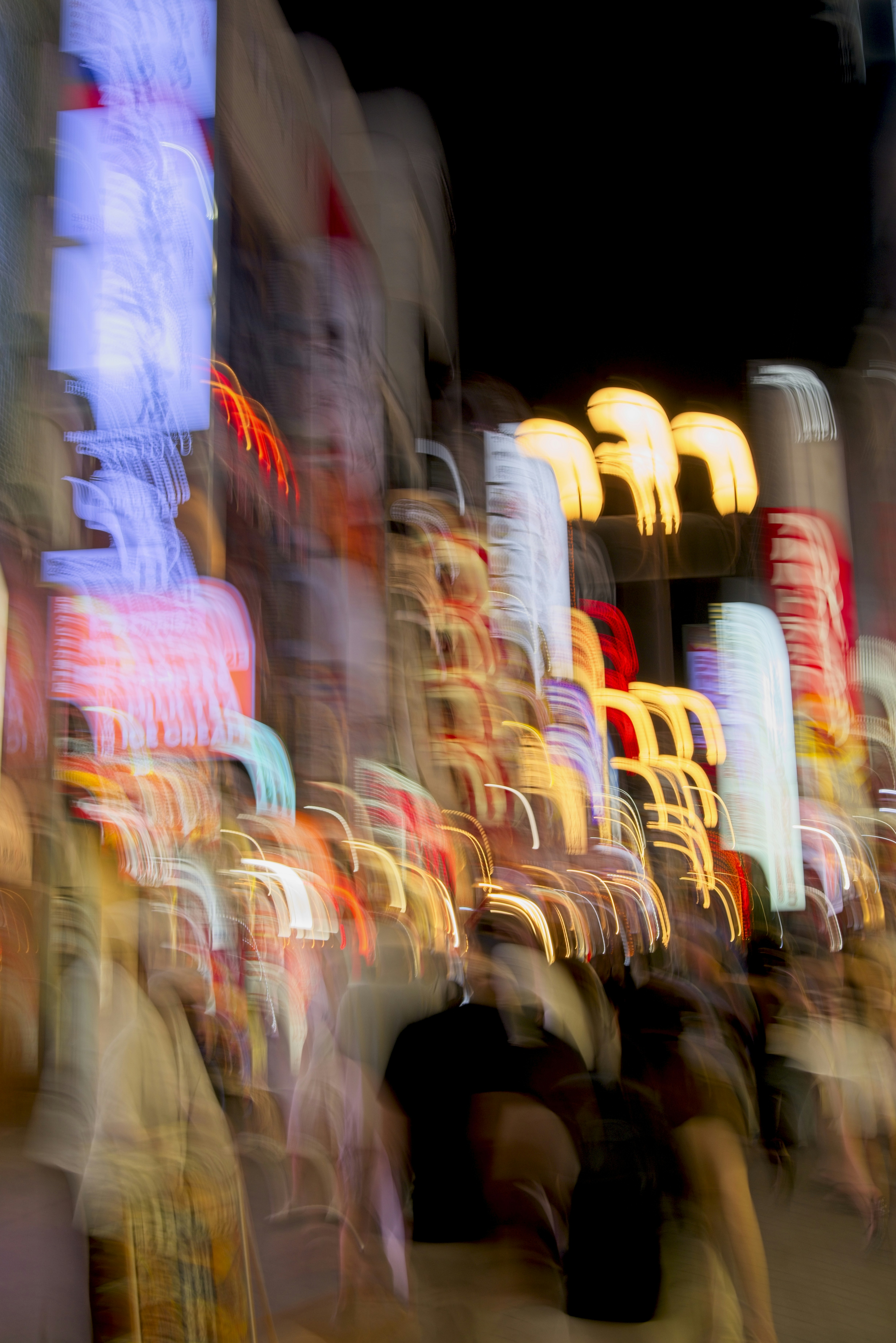 An abstract, energetic long-exposure image transforms the dense neon signage of Dotonbori in Osaka into swirling streaks of gold, red, and white light on a hot summer evening in July. Deliberate camera movement blurs the storefronts and billboards into rhythmic, wave-like patterns, while a single silhouetted figure remains grounded at the base of the frame. The layered, colorful chaos captures the sensory overload and electric energy of Osaka's most iconic entertainment district, offering an experimental, painterly interpretation of its nighttime glow.