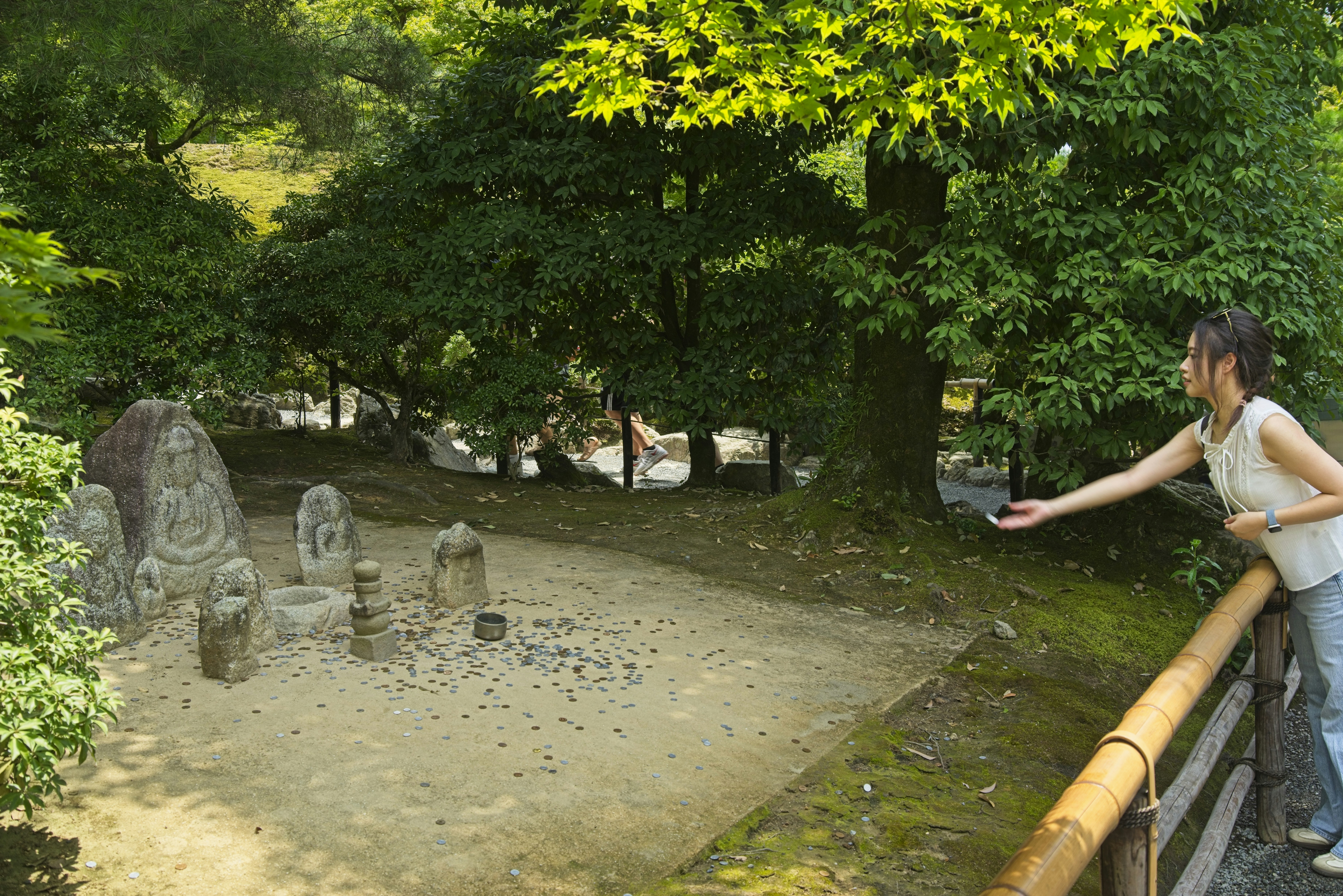 Playful Throw: A Visitor Reaches Toward a Row of Stone Statues in a Shaded Japanese Garden