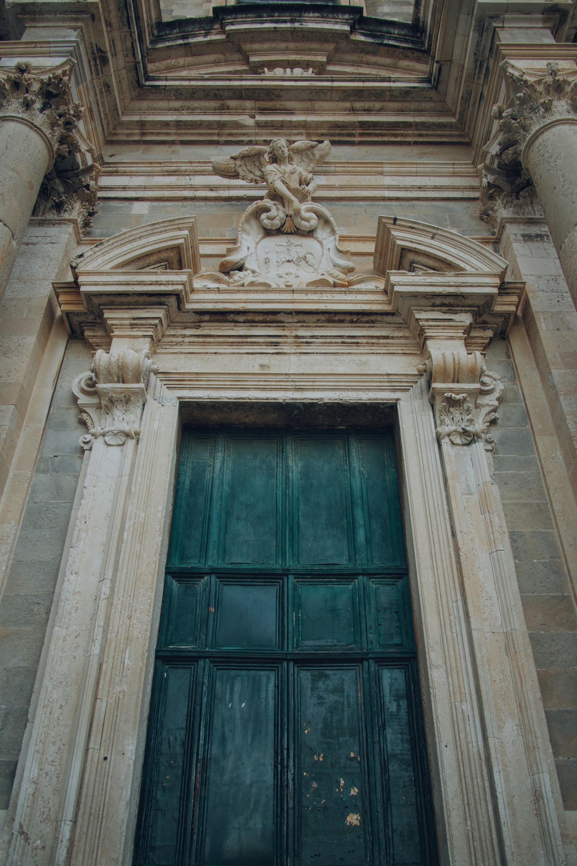 A dark green wooden door set within an ornate stone archway with a carved angel.