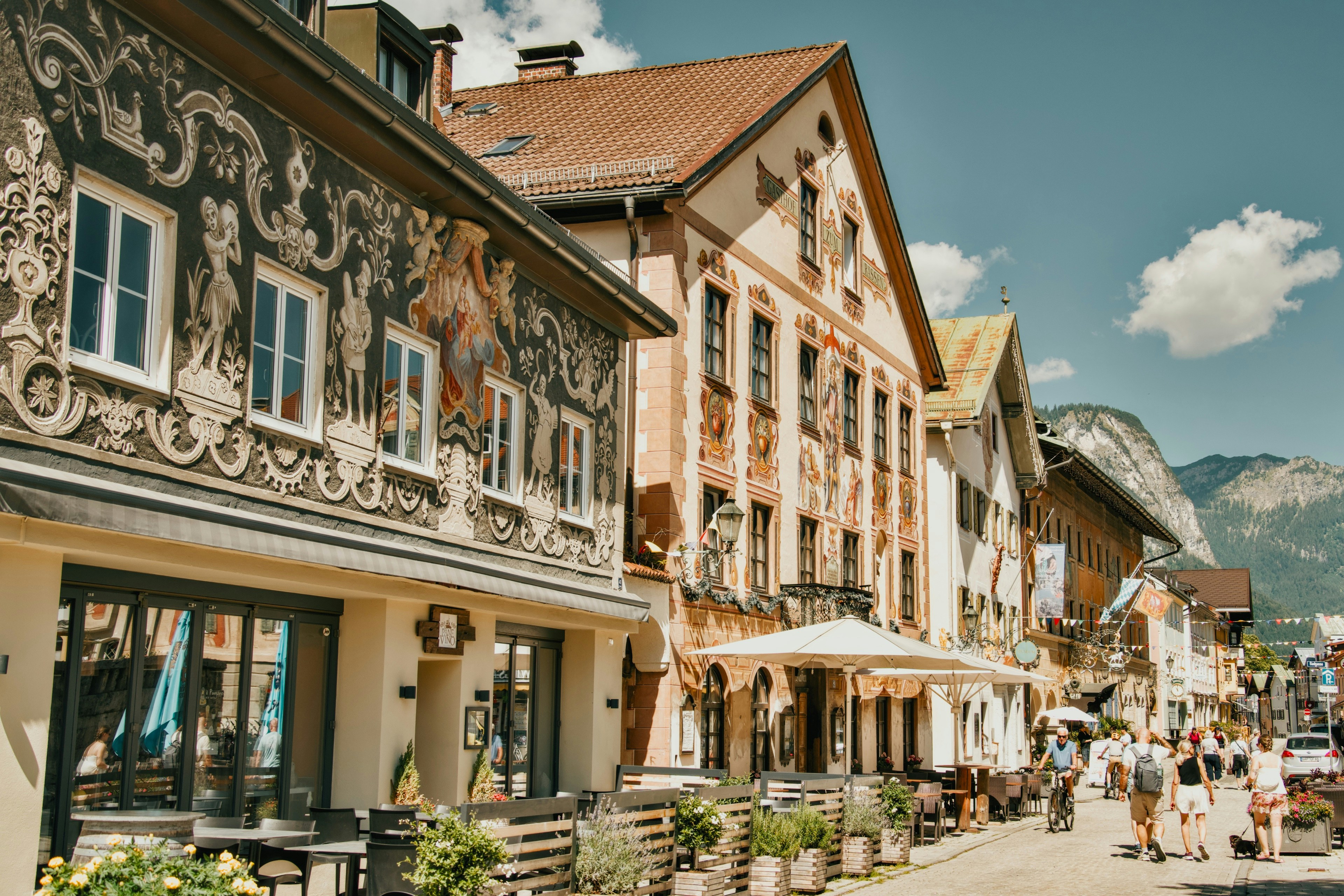 Sunlit Alpine Street: Painted Facades and Strolling Market