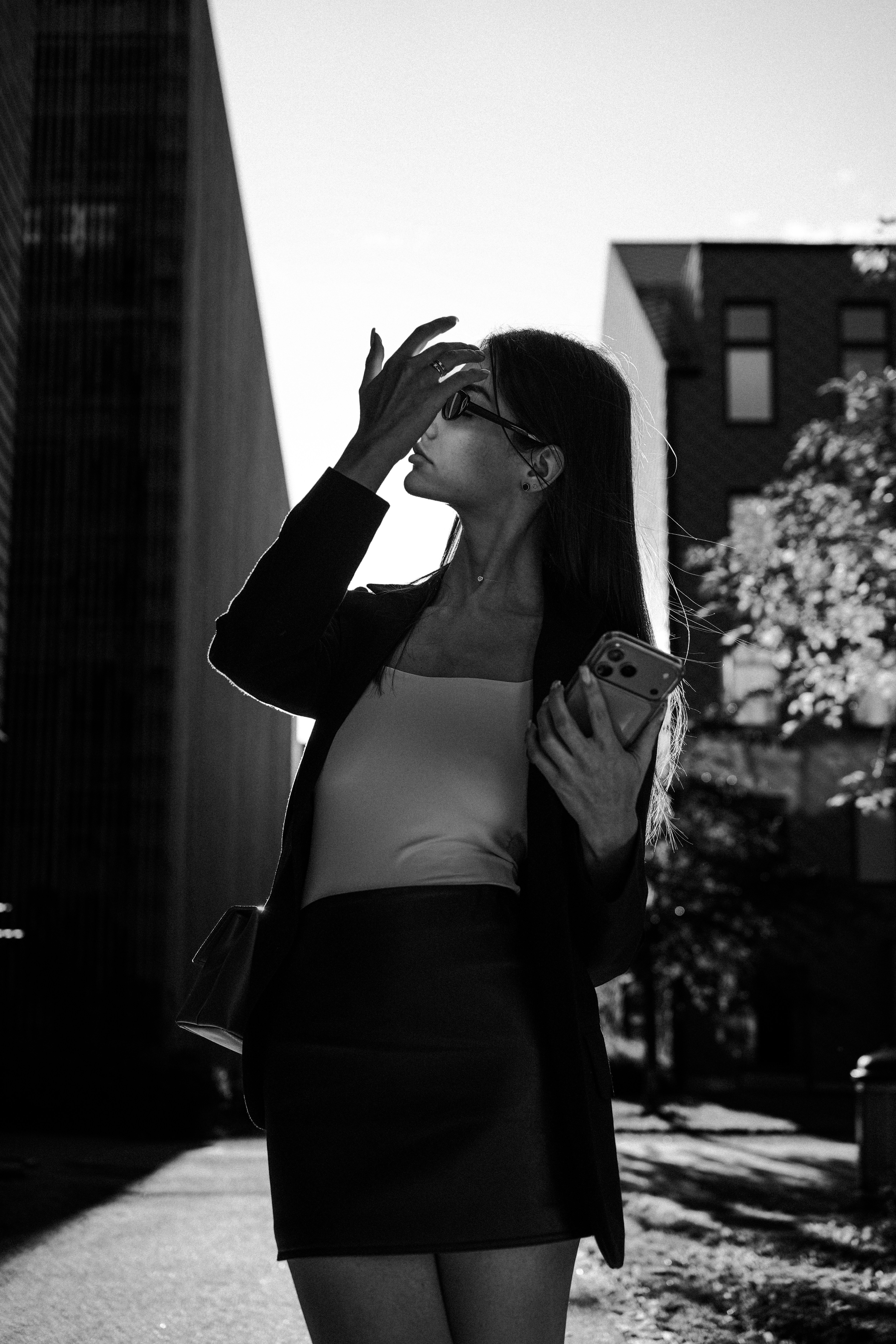 A woman in a blazer and skirt holding a smartphone on a city street.