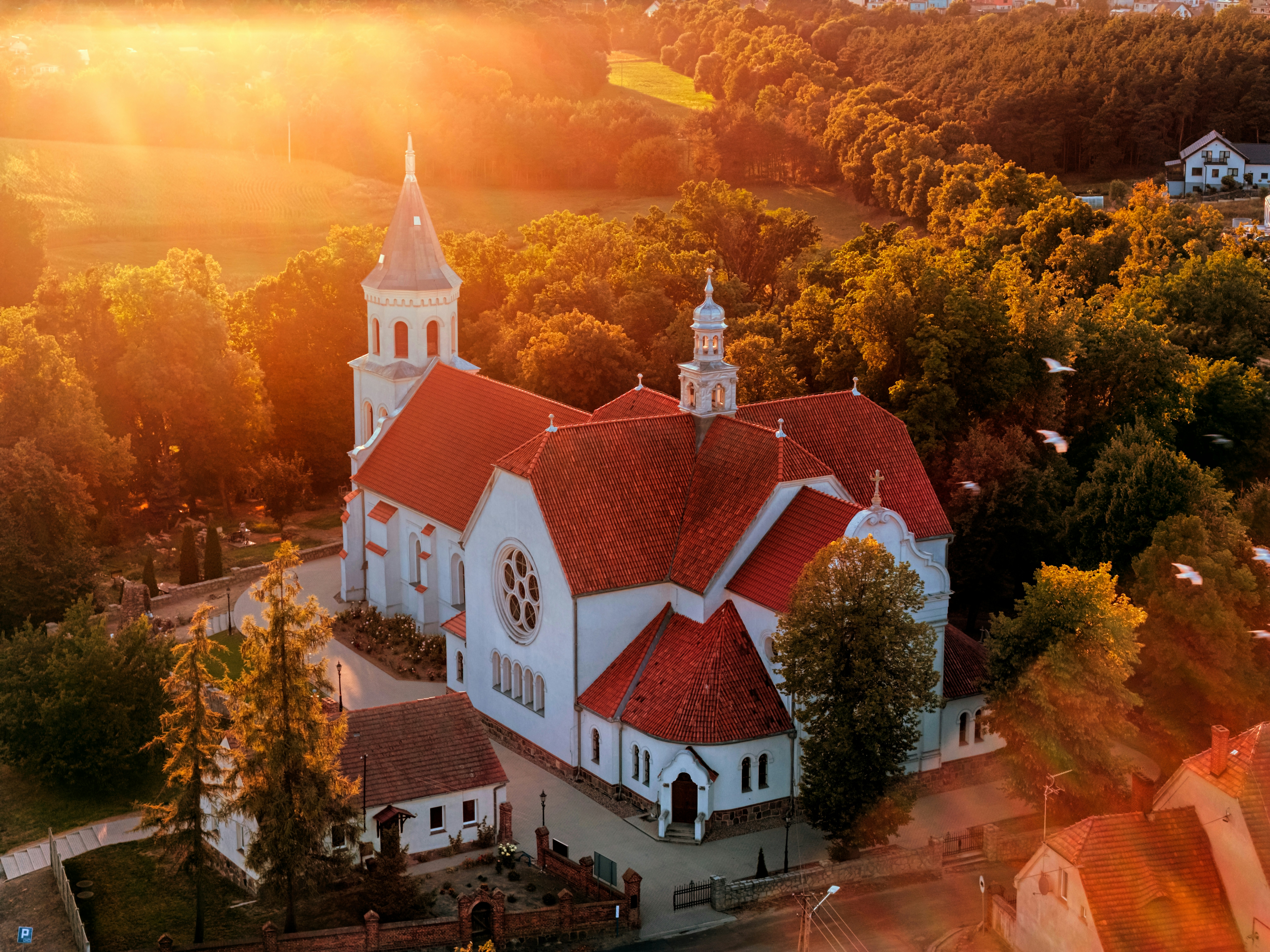 Golden Hour Cathedral: Aerial Glimpse of a Tiled Church Surrounded by Autumn Canopy