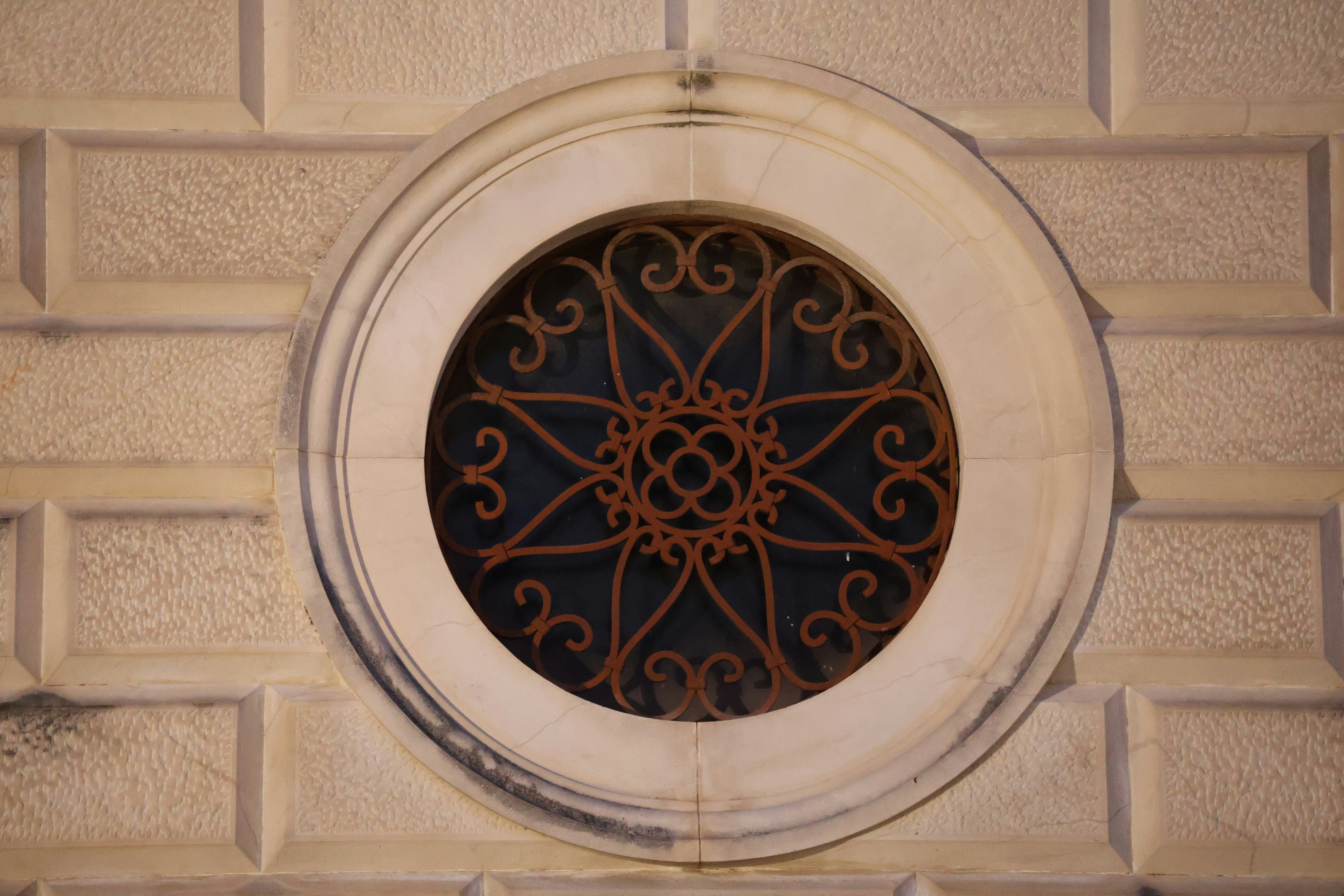 Circular stone window framed by ornate wrought-iron lattice embedded in a textured facade