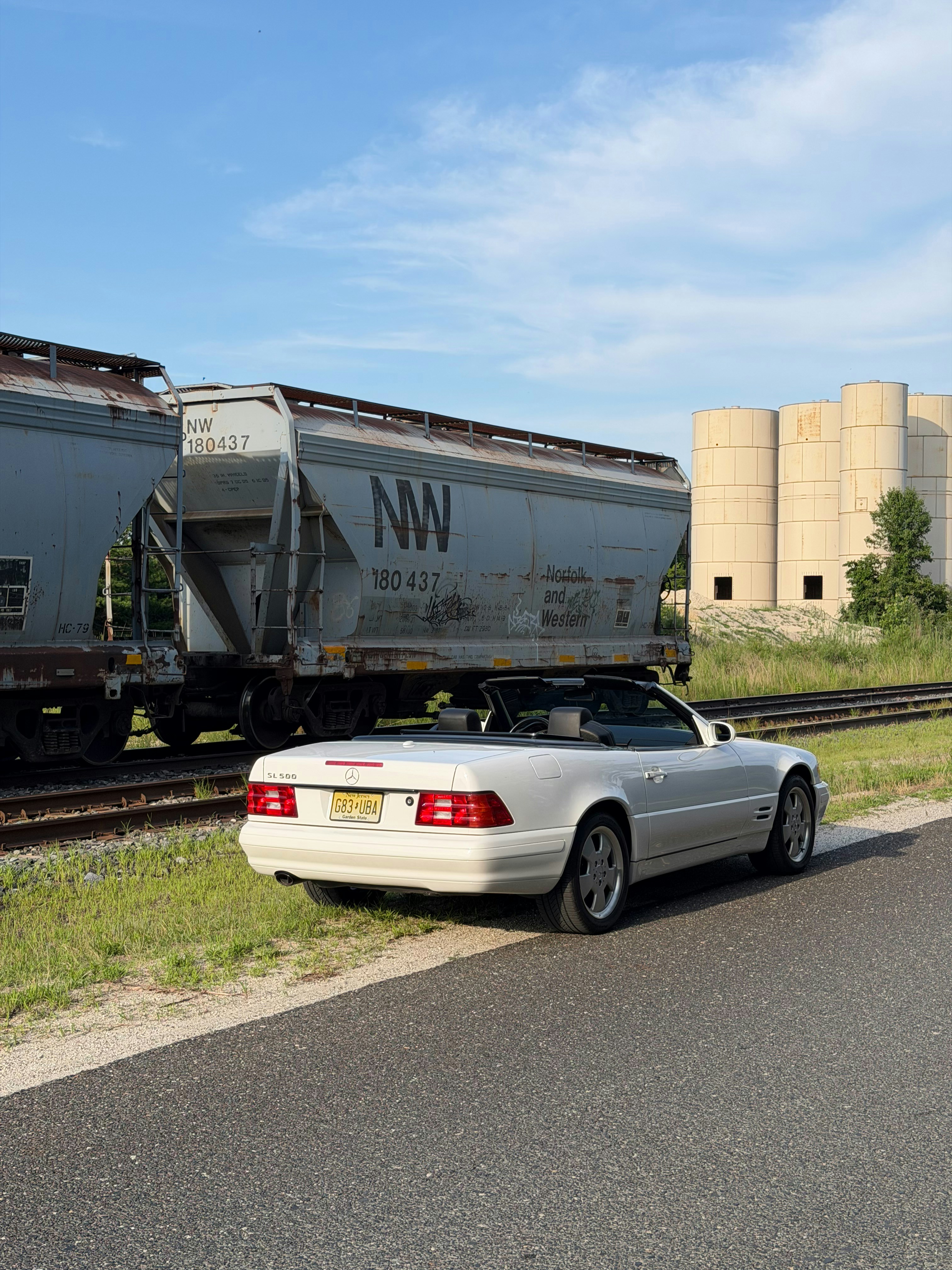 Convertible under the Tracks: White sports car by rusted freight cars