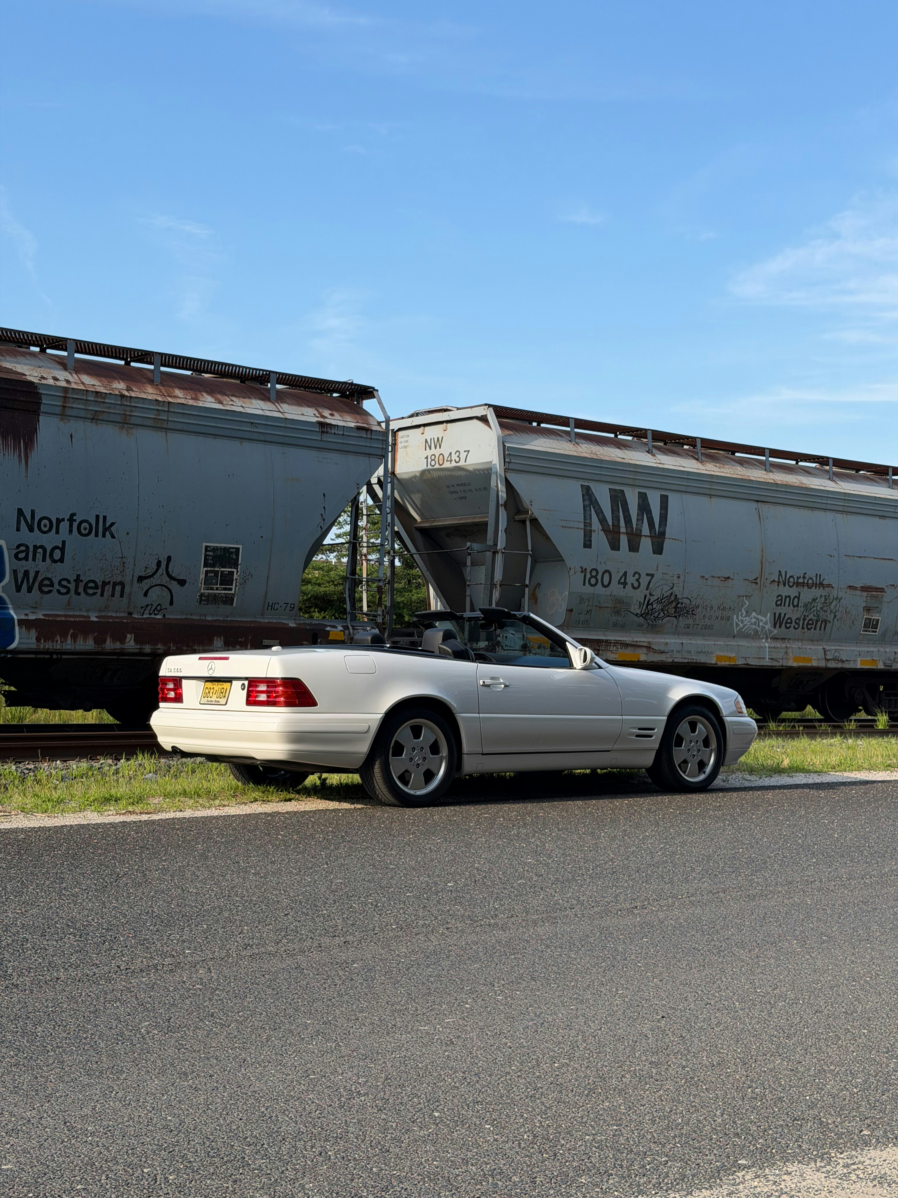 White convertible by freight cars under a clear blue sky