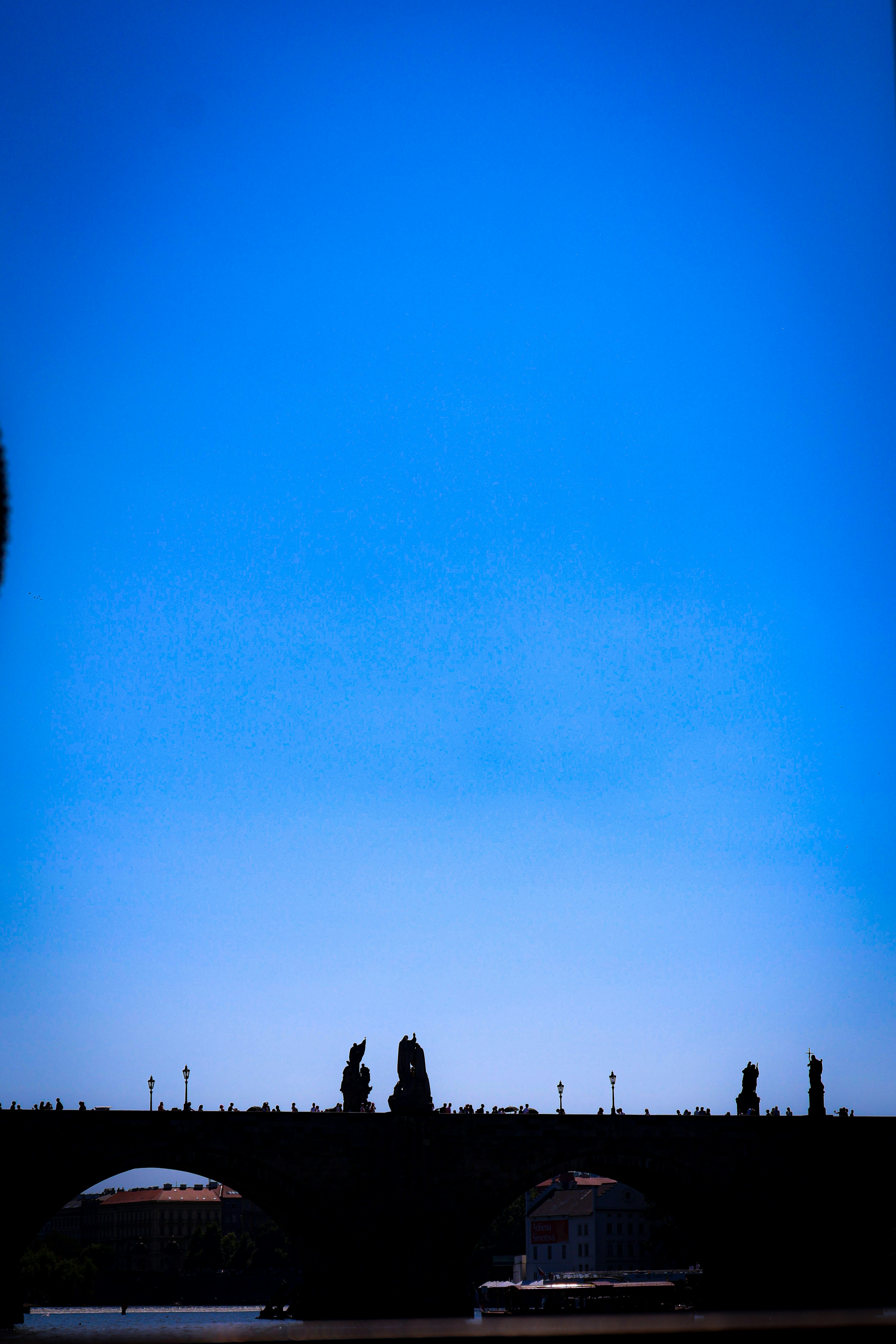 Silhouette of a historic bridge crowned by statues beneath a vast cerulean sky