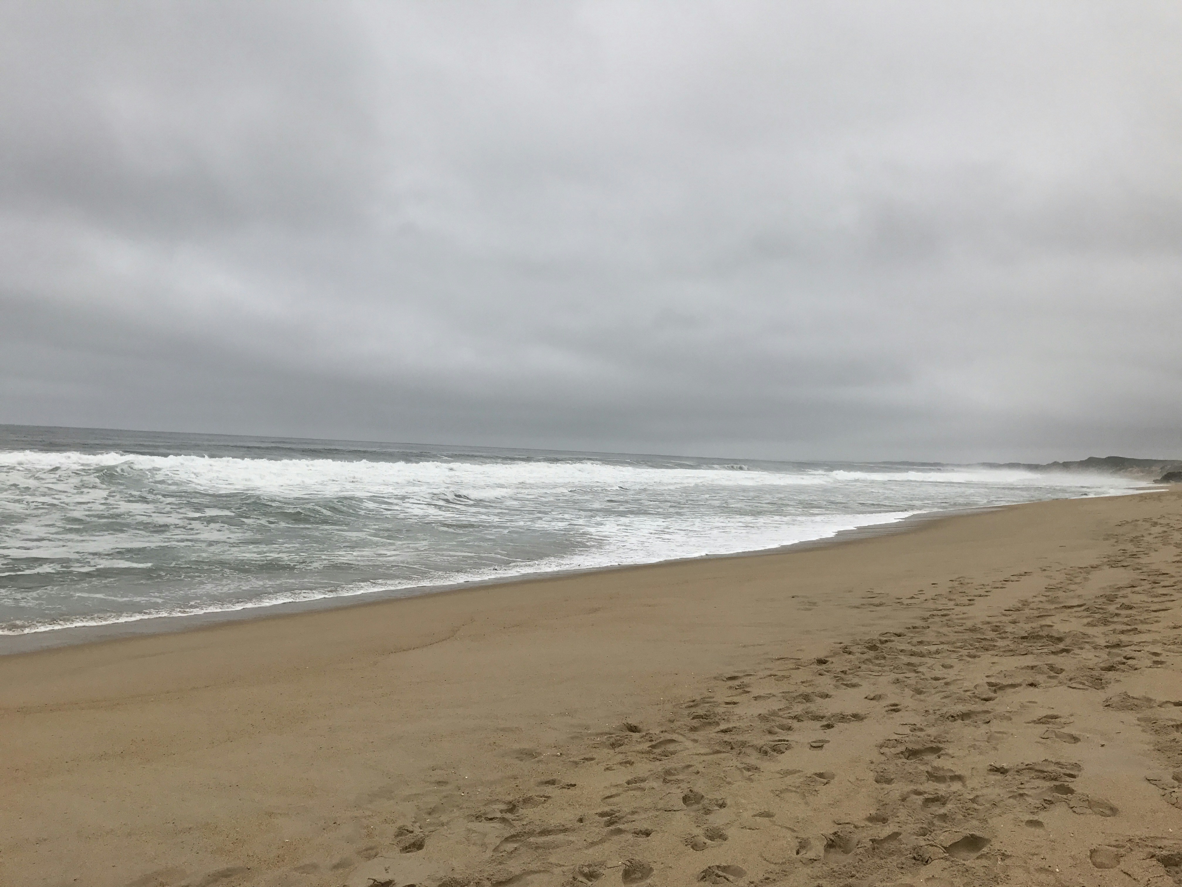 Overcast Shoreline: Footprints and Foam Along a Quiet Beach