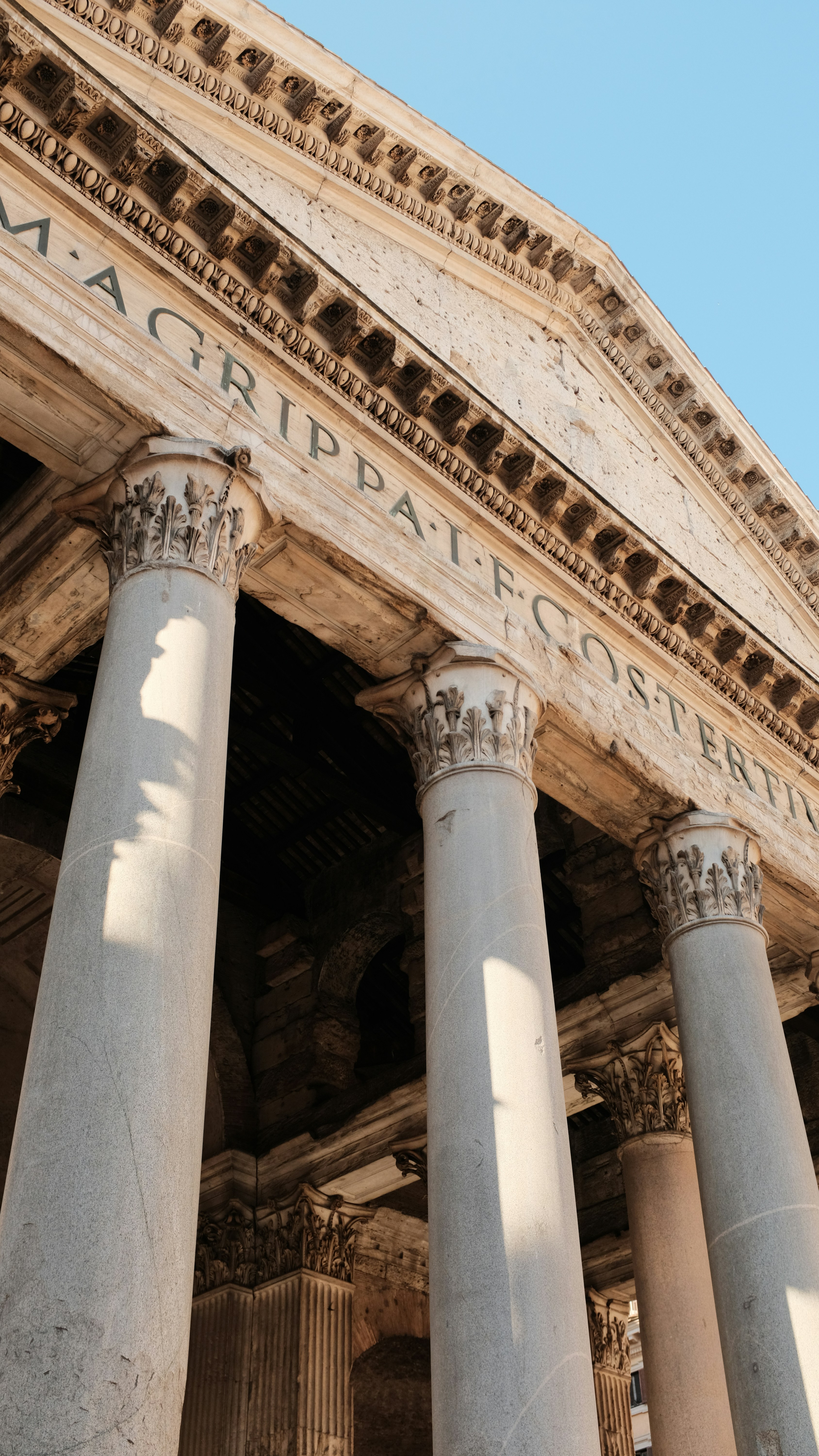 Columned facade with carved capitals bathed in warm light, revealing stone textures and classical inscriptions.