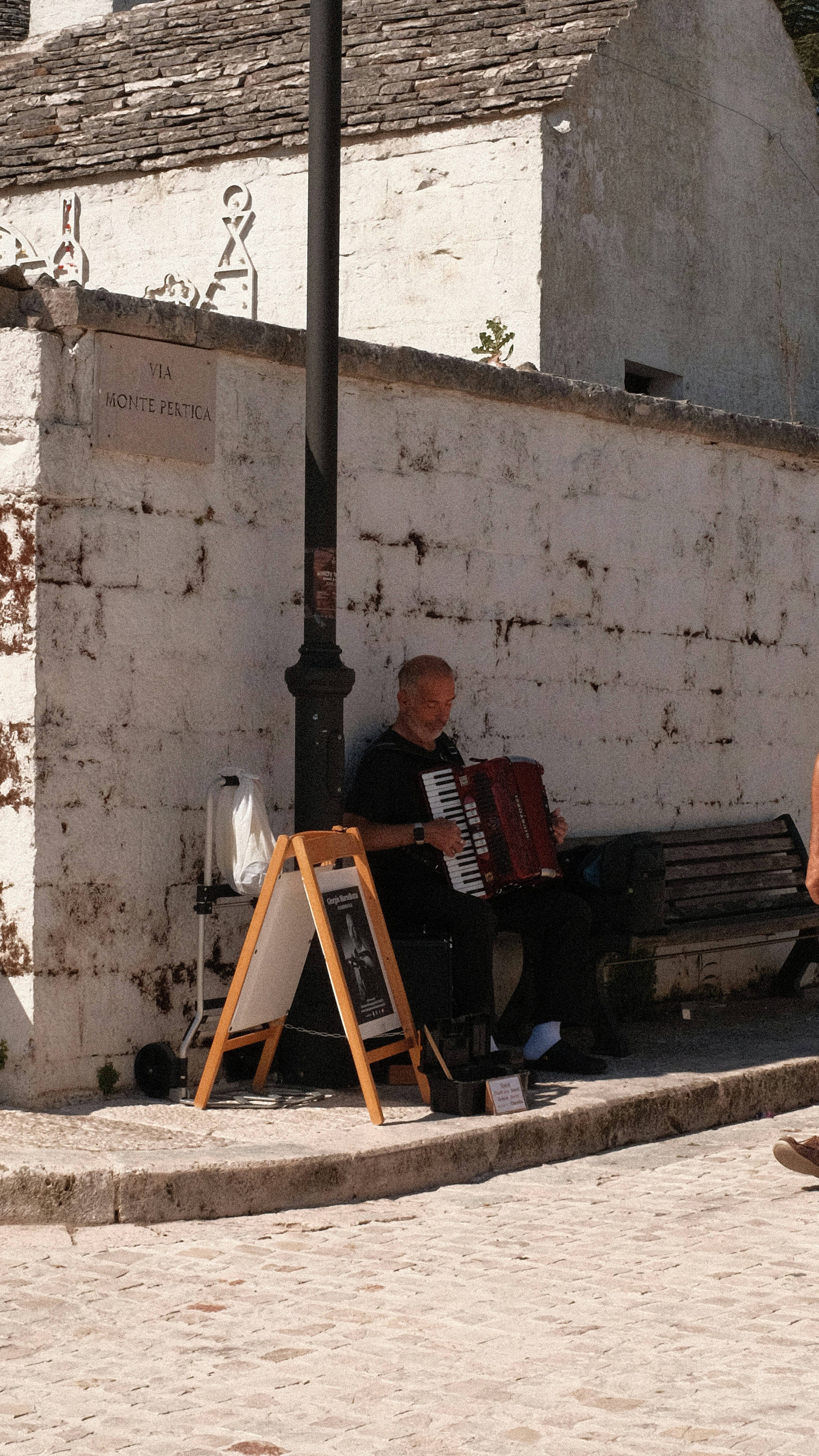 Street musician in sunlight: accordionist by a stone wall