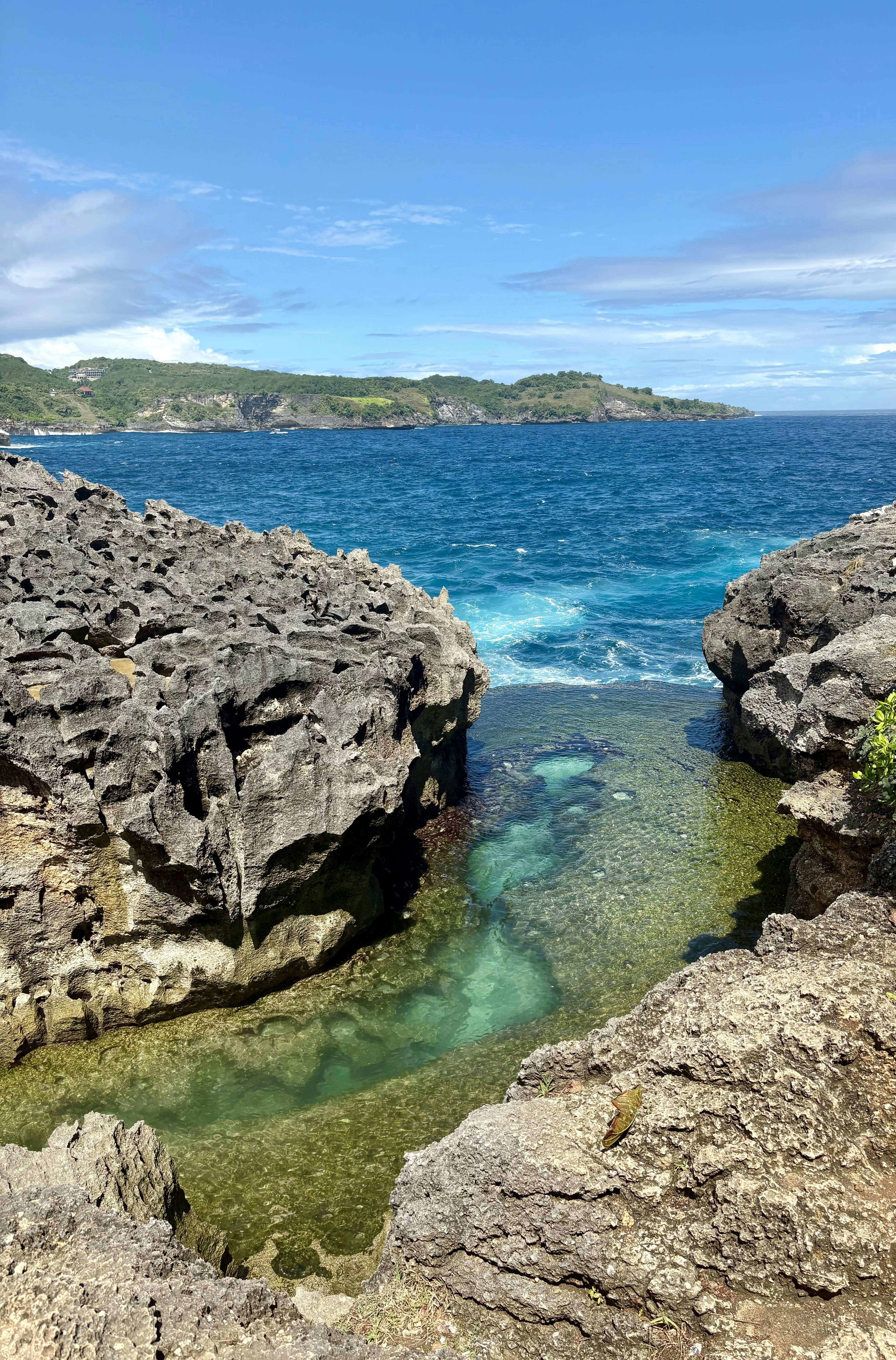Turquoise tidal pools nestled between rugged basalt cliffs meet a deep blue sea under a bright, clear sky.