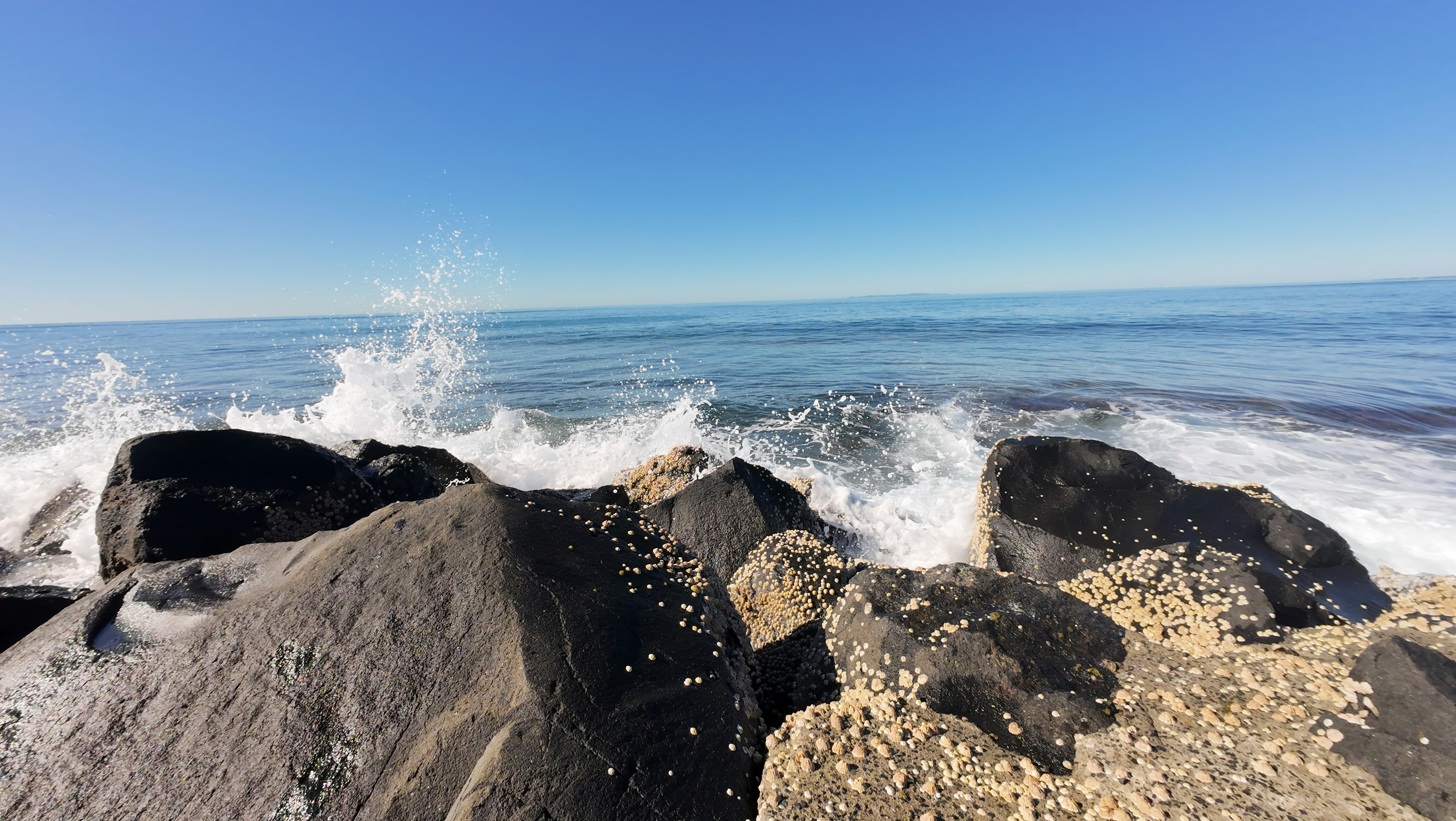 Rock-tide Crest: Waves Exploding Over Coastal Boulders Under a Clear Sky