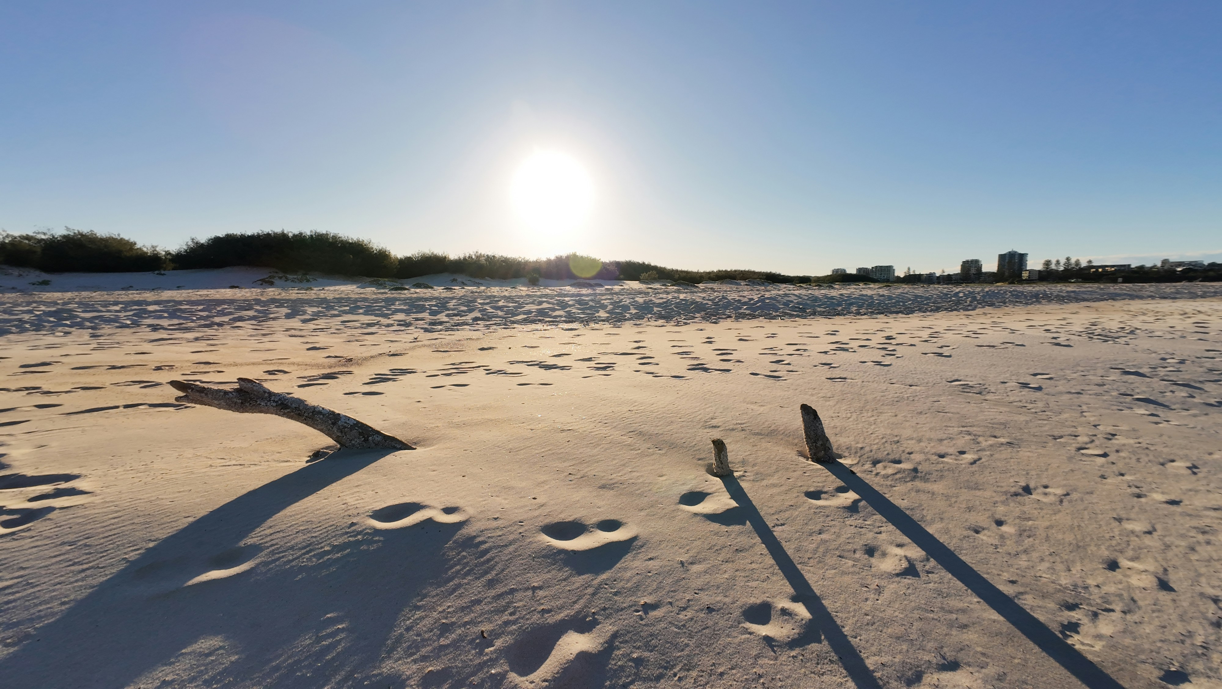 Sunlit Shore Shadows: Footprints and Distant Skyline