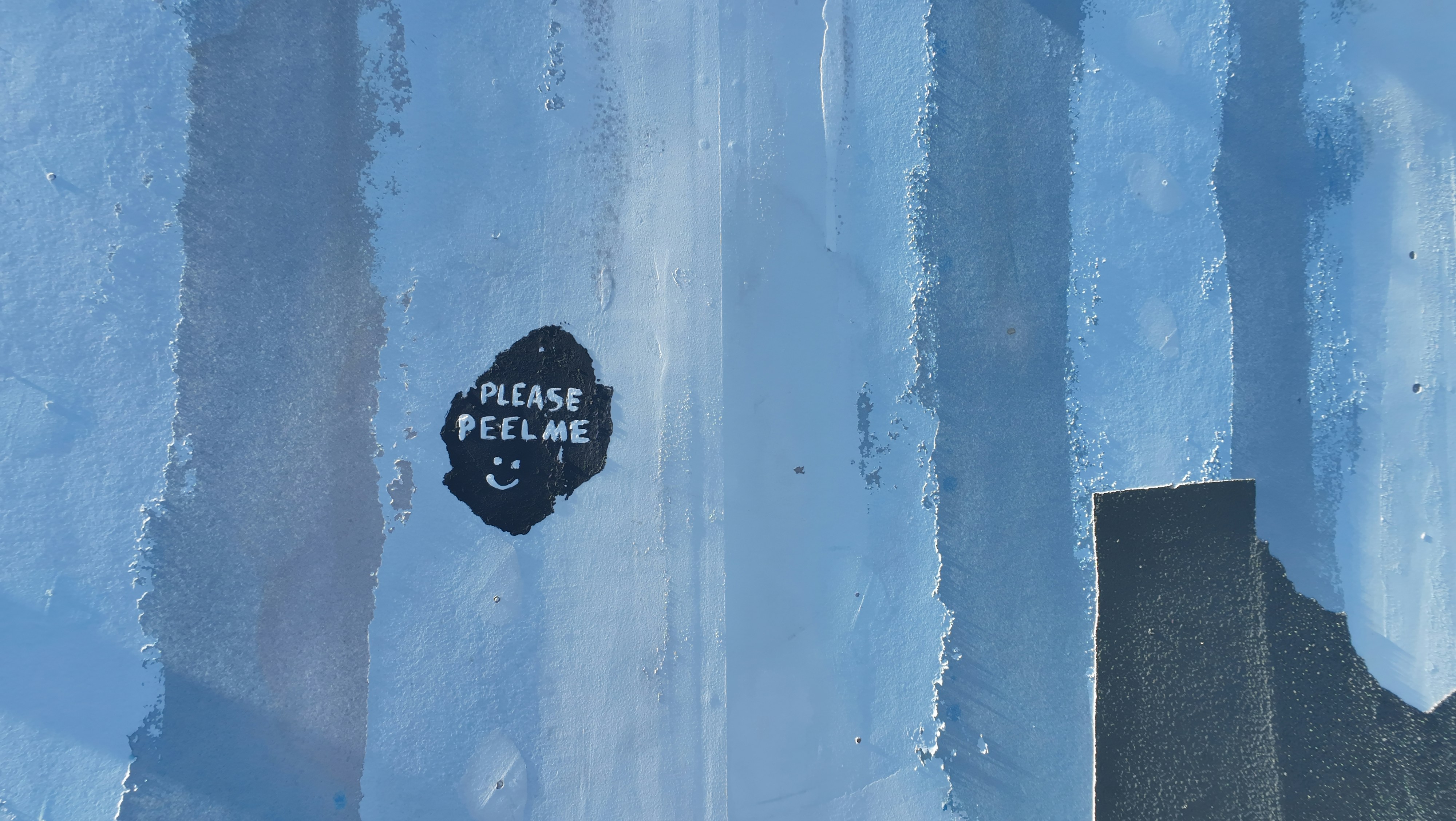 Blue mural with a small black circle bearing a smiley face and the text "PLEASE FEEL ME"