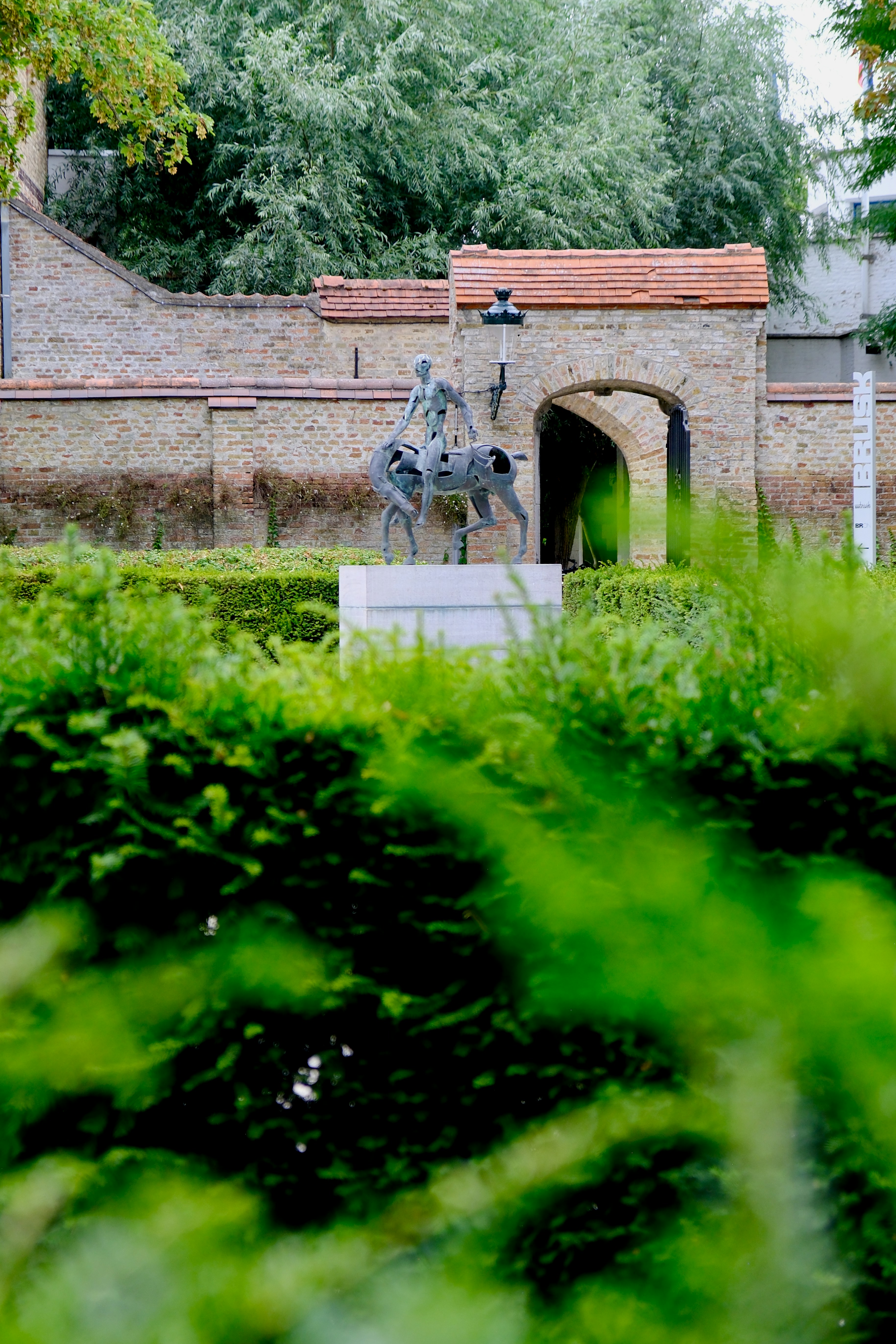 Statue in the Garden Gate: A bronze trio under a brick arch
