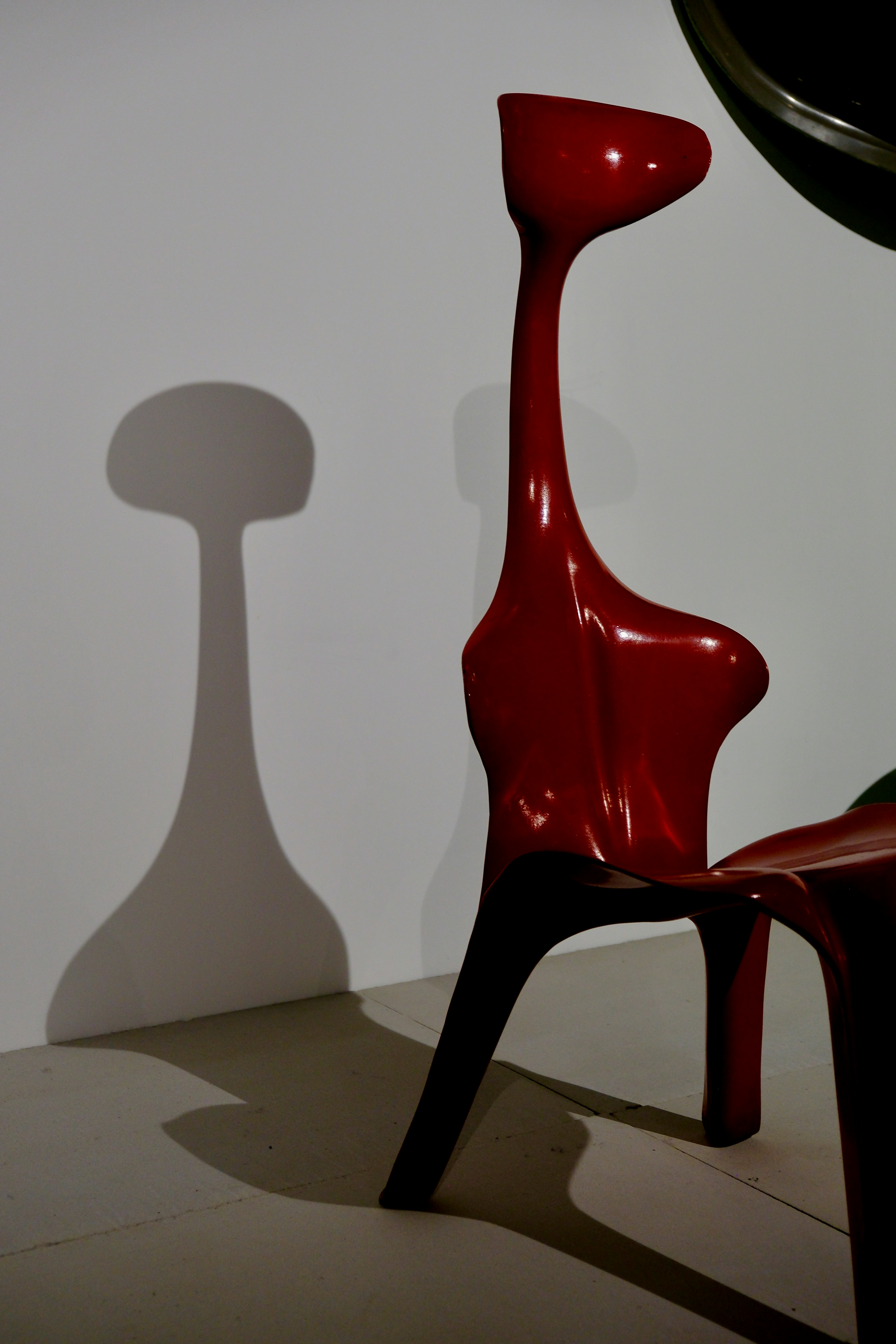 Red sculpted chair casting bold shadows on a white gallery wall