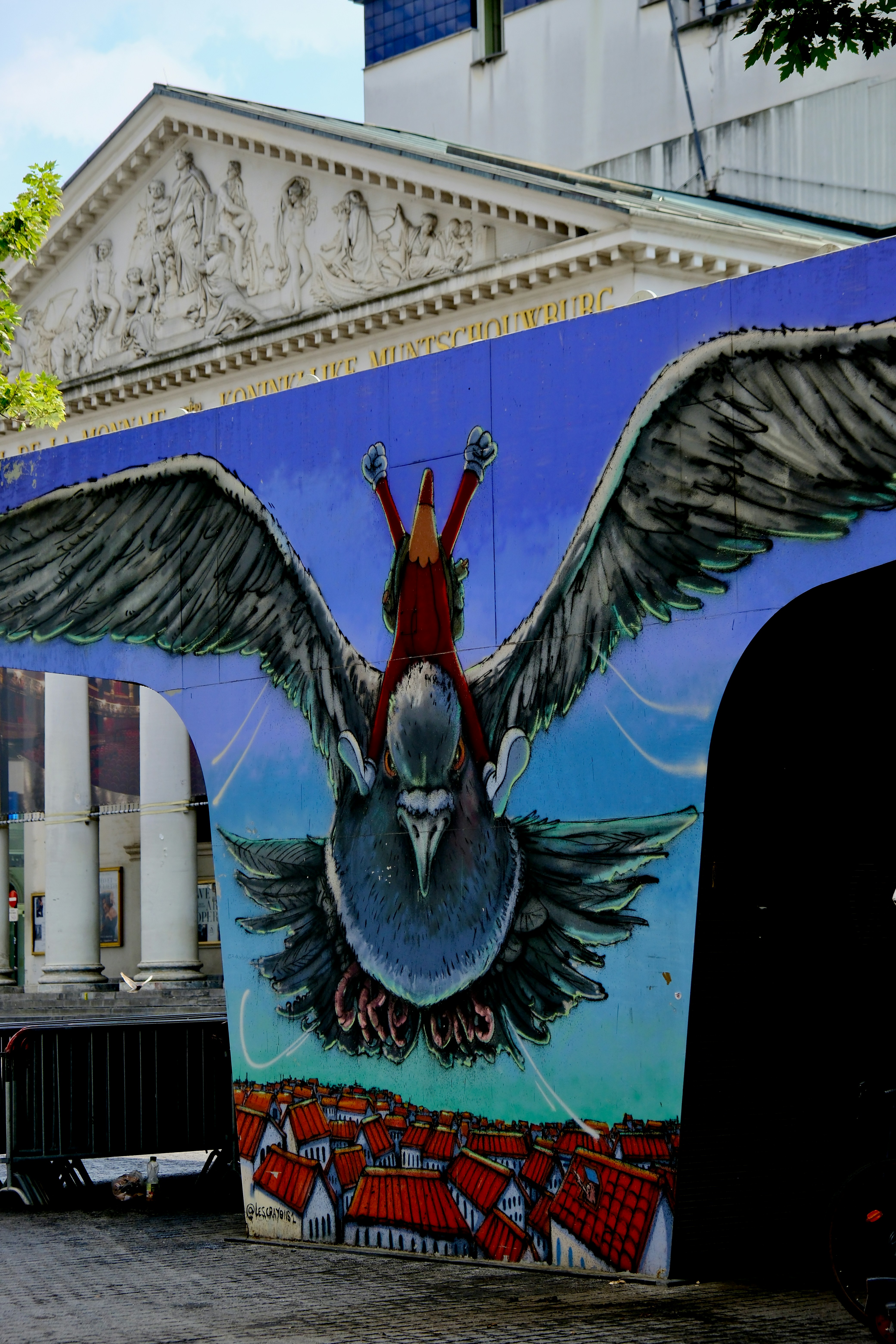 Winged mural gateway: a blue rooster soars above a painted alley