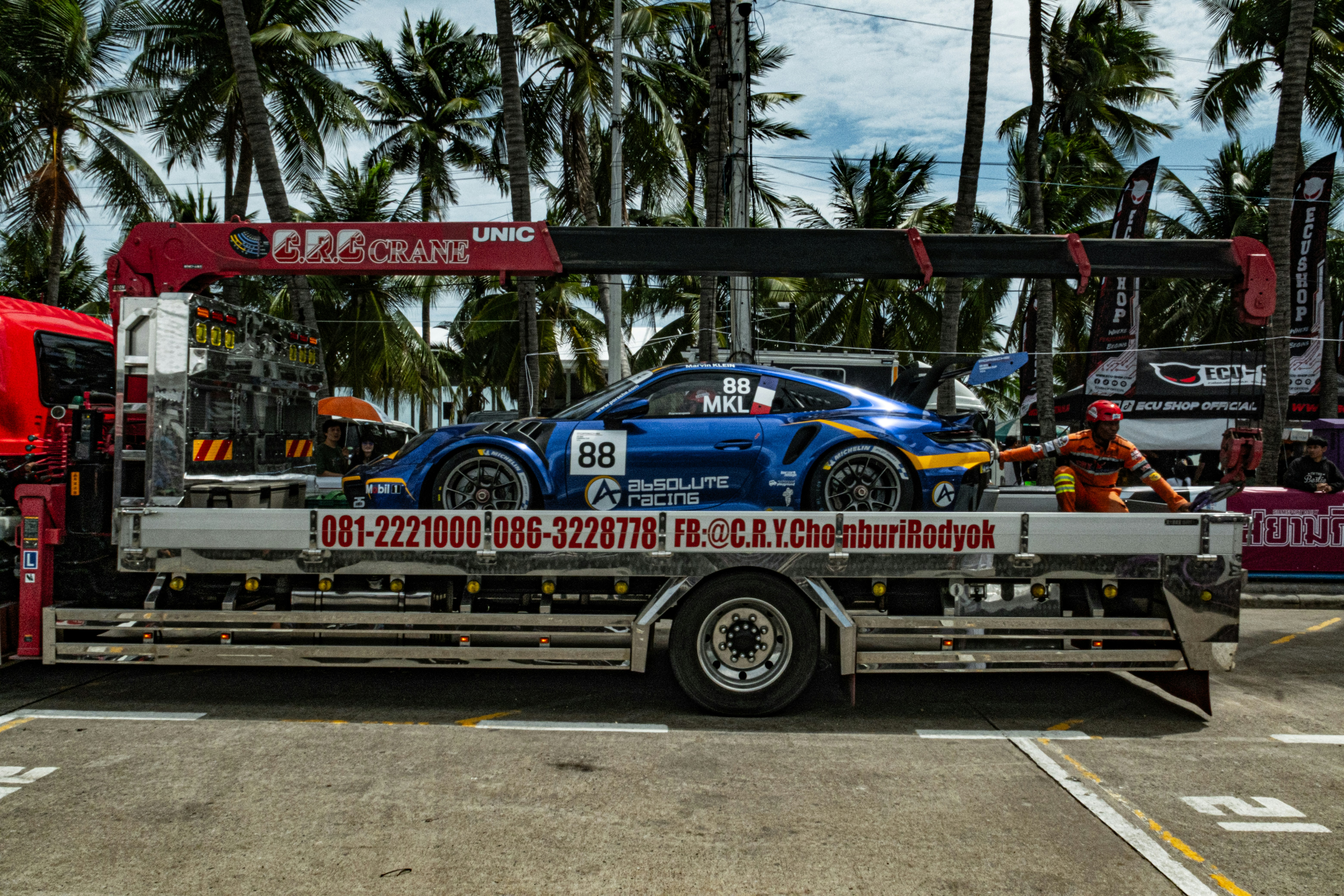 Blue race car on a flatbed trailer during a sunlit event