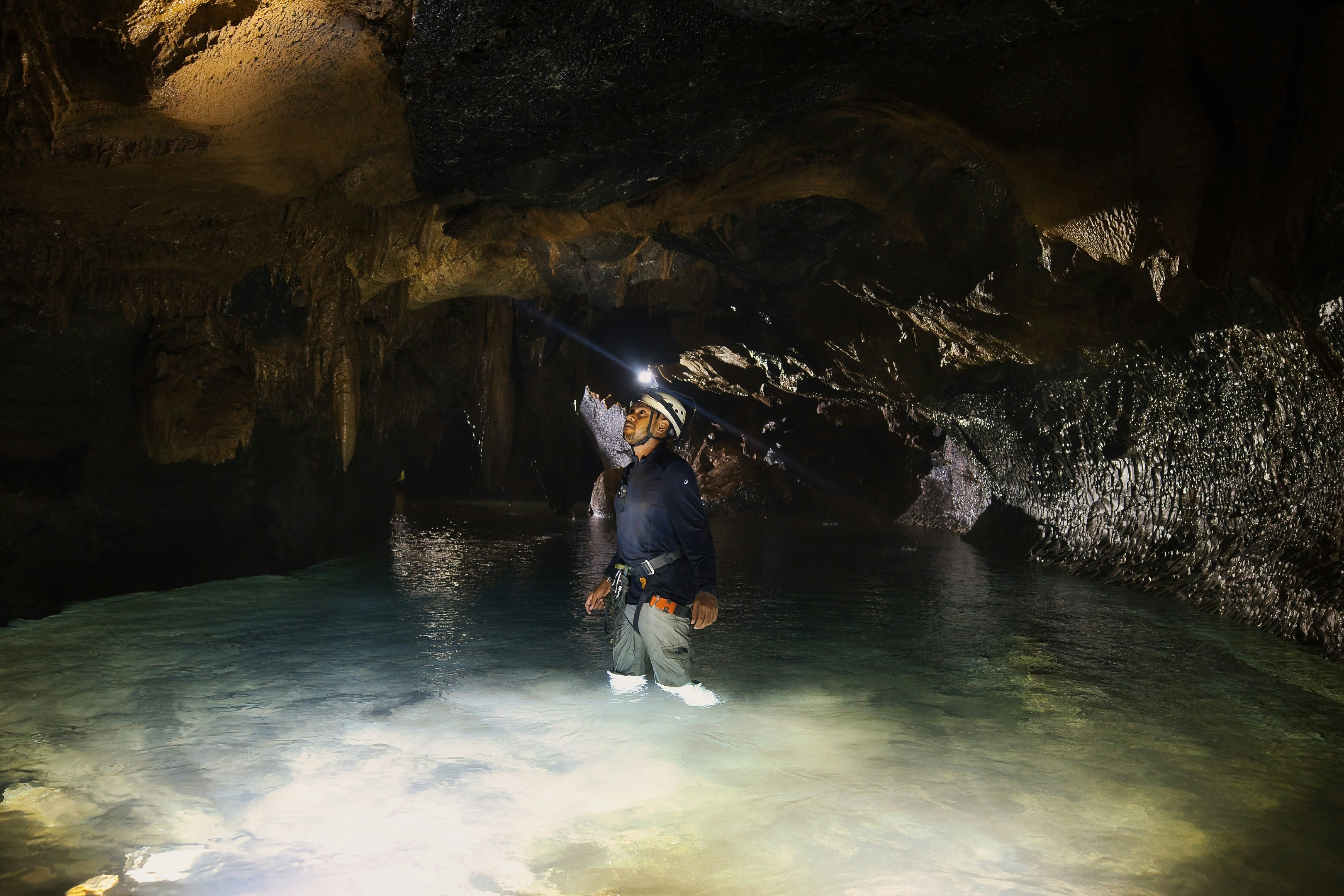 A lone explorer illuminates a cavern pool with a headlamp glow