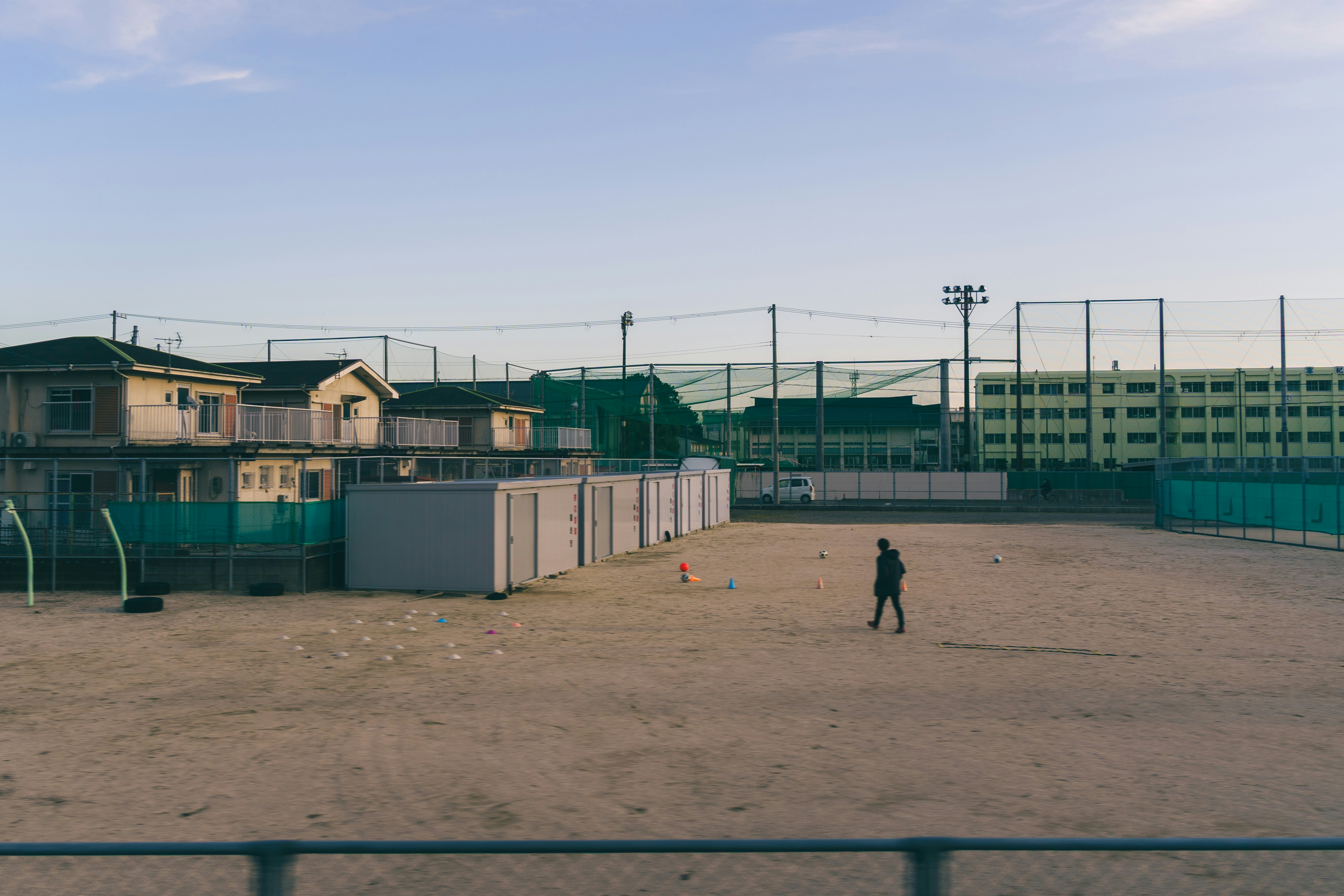 Solitary figure on a sunlit field behind a quiet urban playground