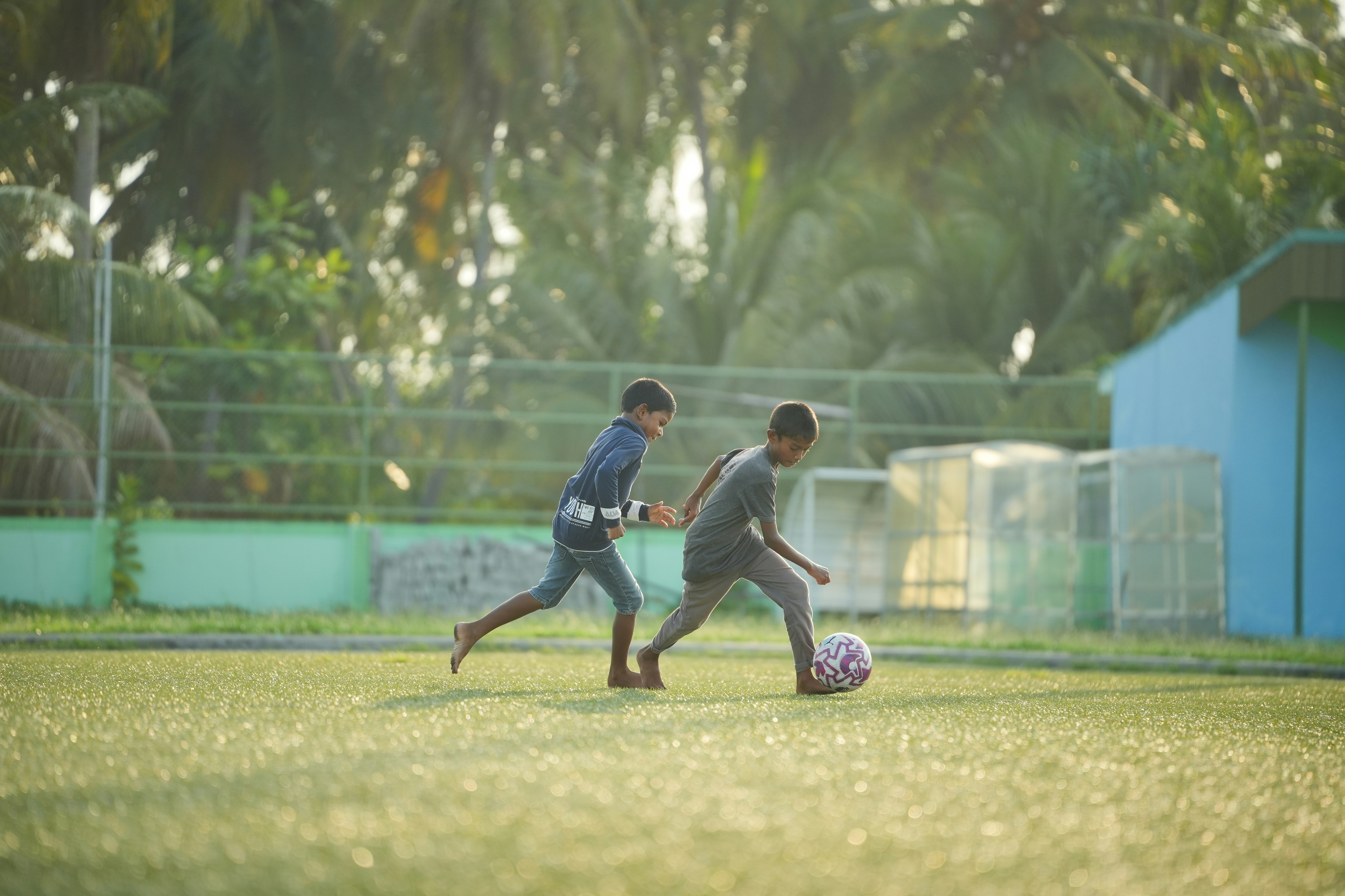 Two Young Players Chase a Spinning Ball on a Sunlit Field