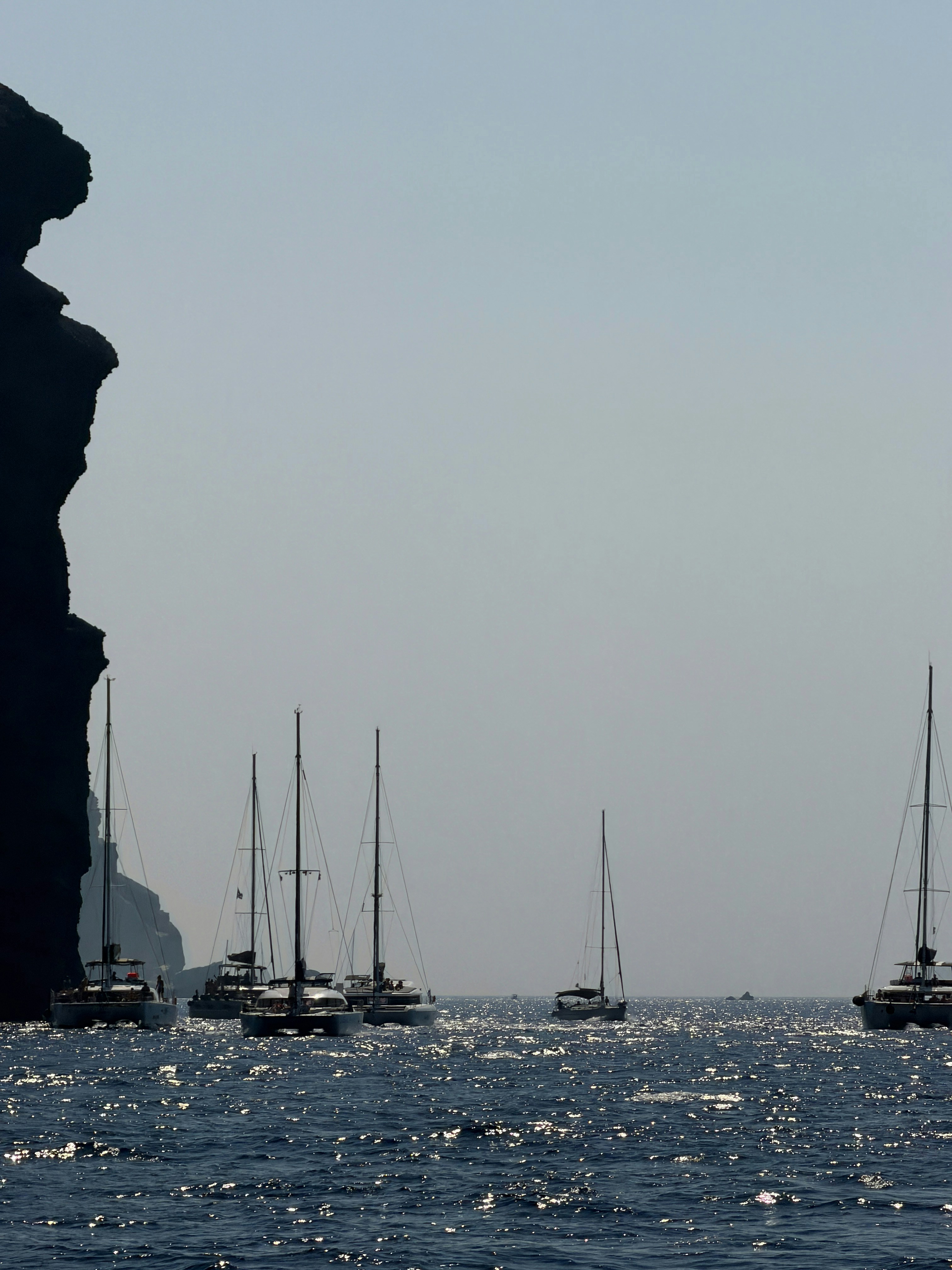 Cliffs, Sails, and Sea: Boats at Dusk by the Rock