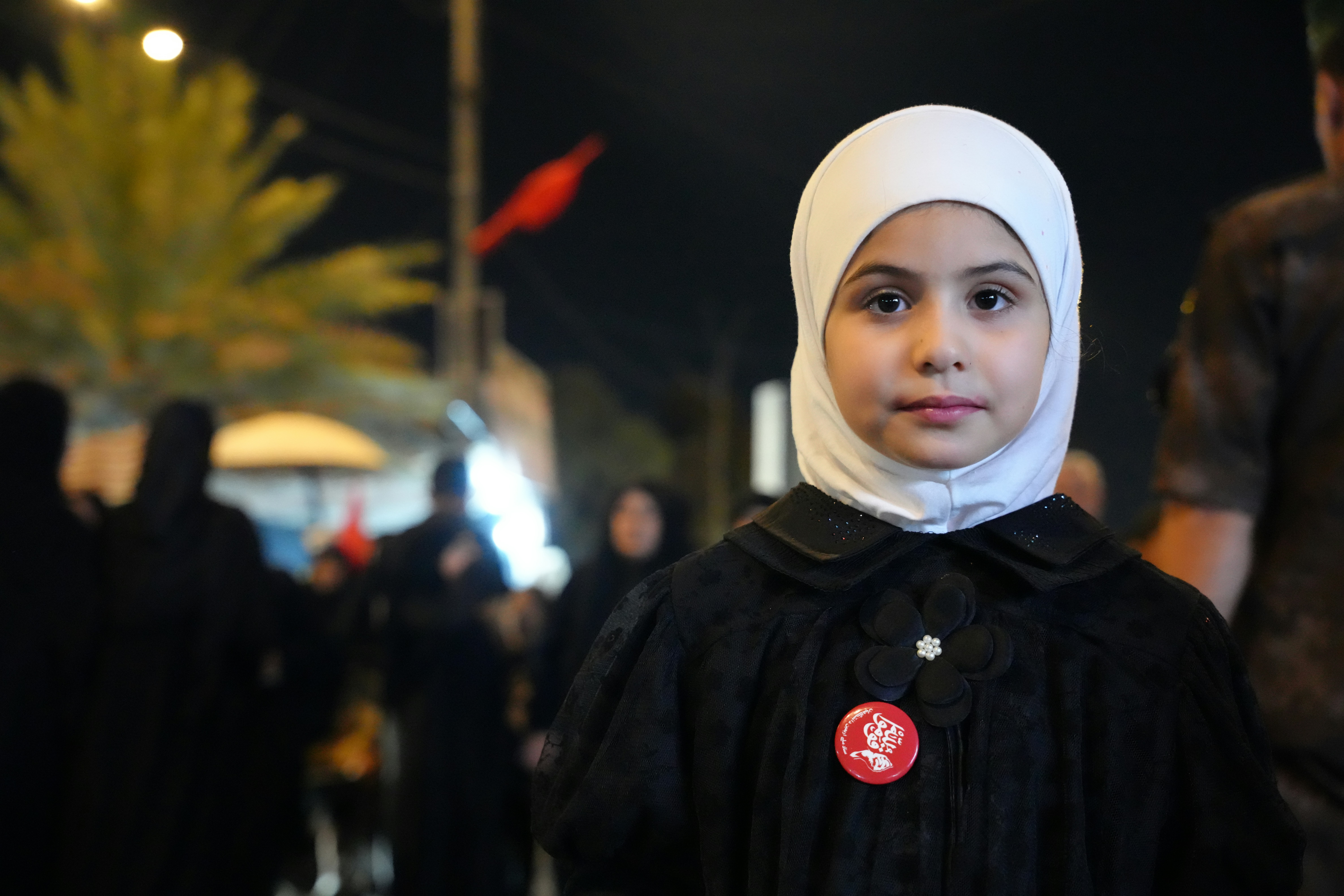 A young girl in a white hijab and black dress at night