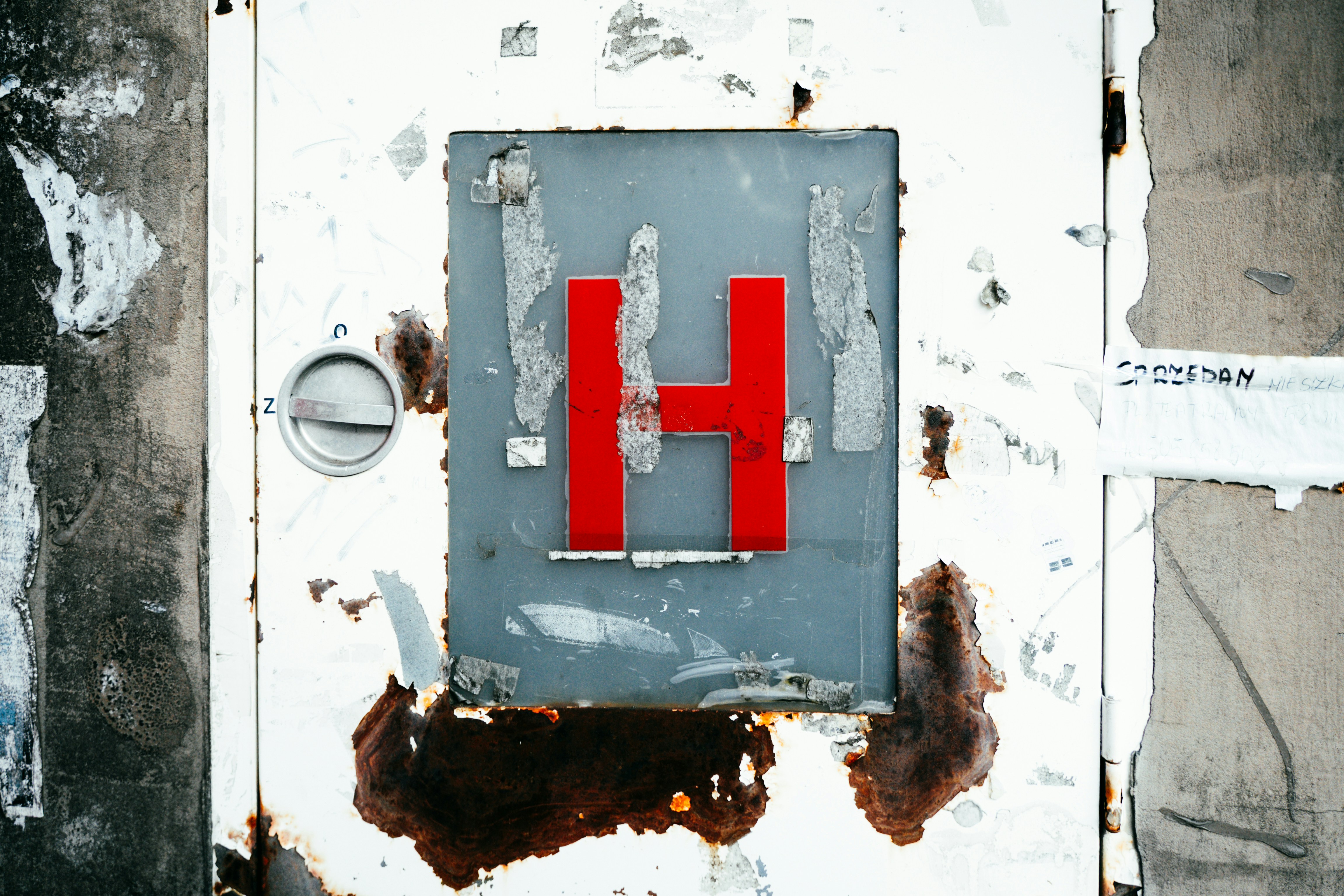 Weathered industrial emblem: a bold red H set in a rusty gray box