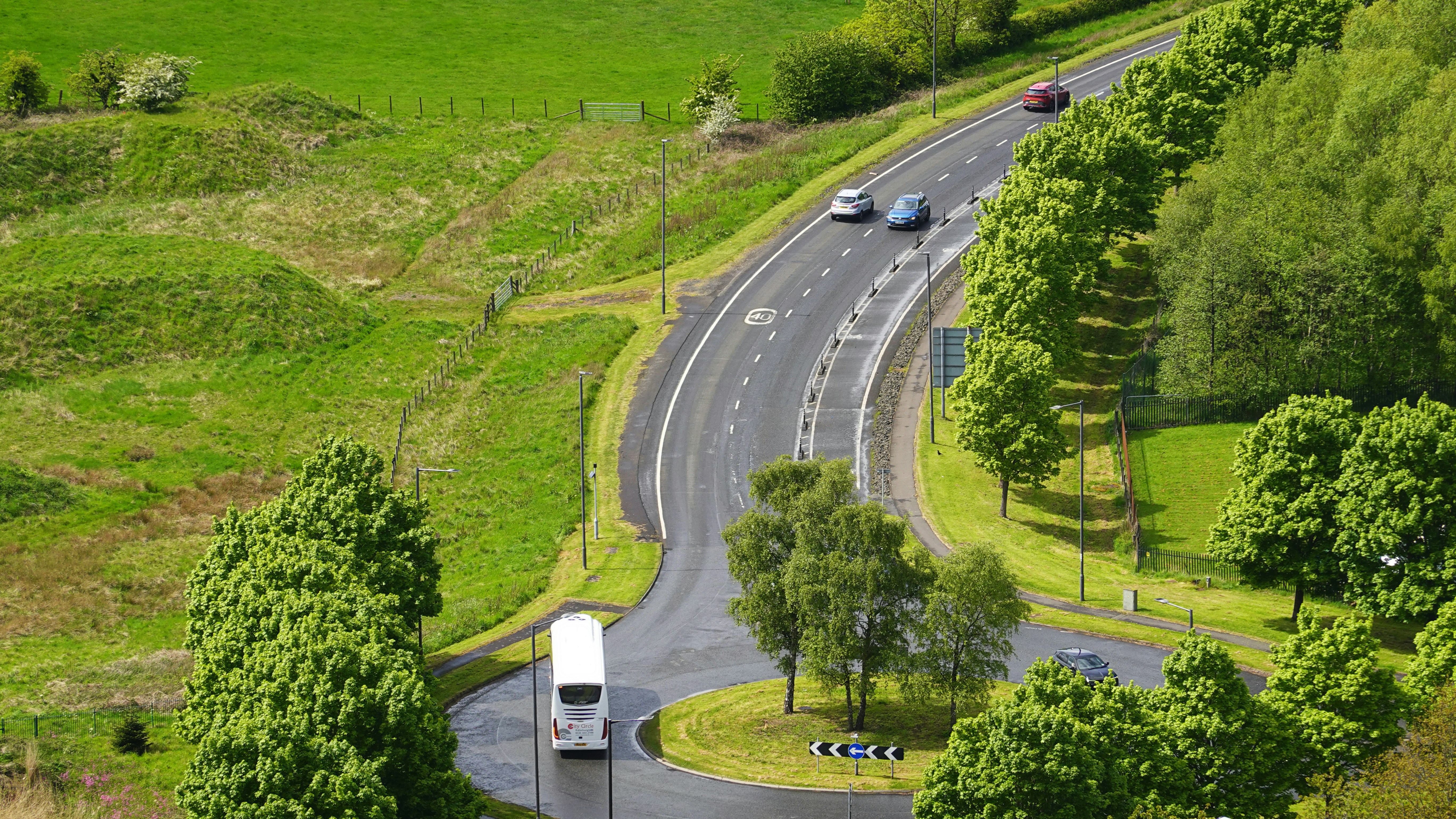 A Quiet Climb: Cars navigate a winding parkway through sunlit greenery