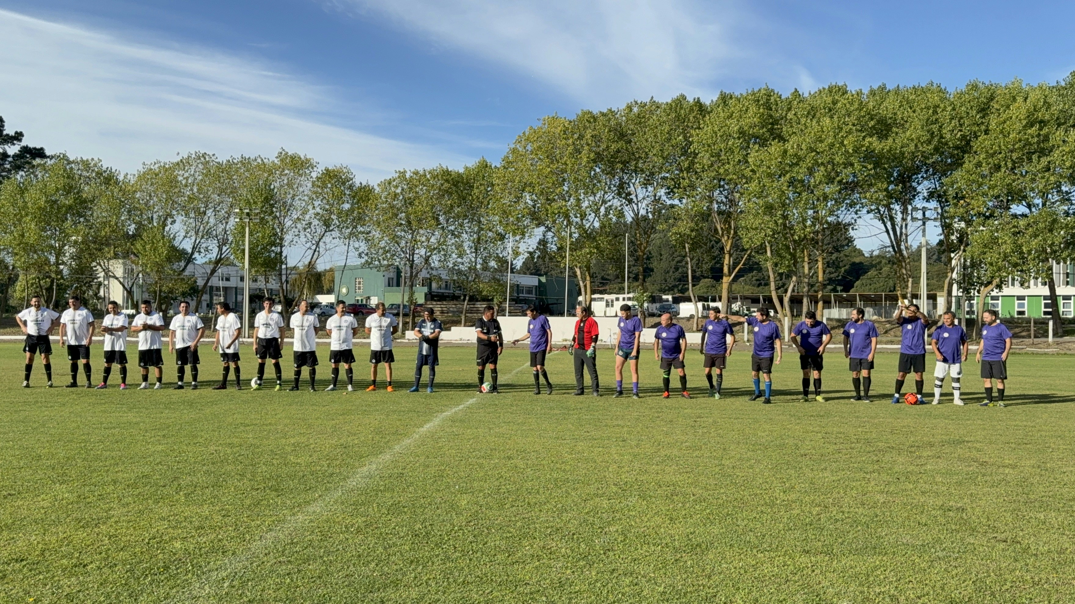 Line of players under a sunlit treetop canopy before kickoff