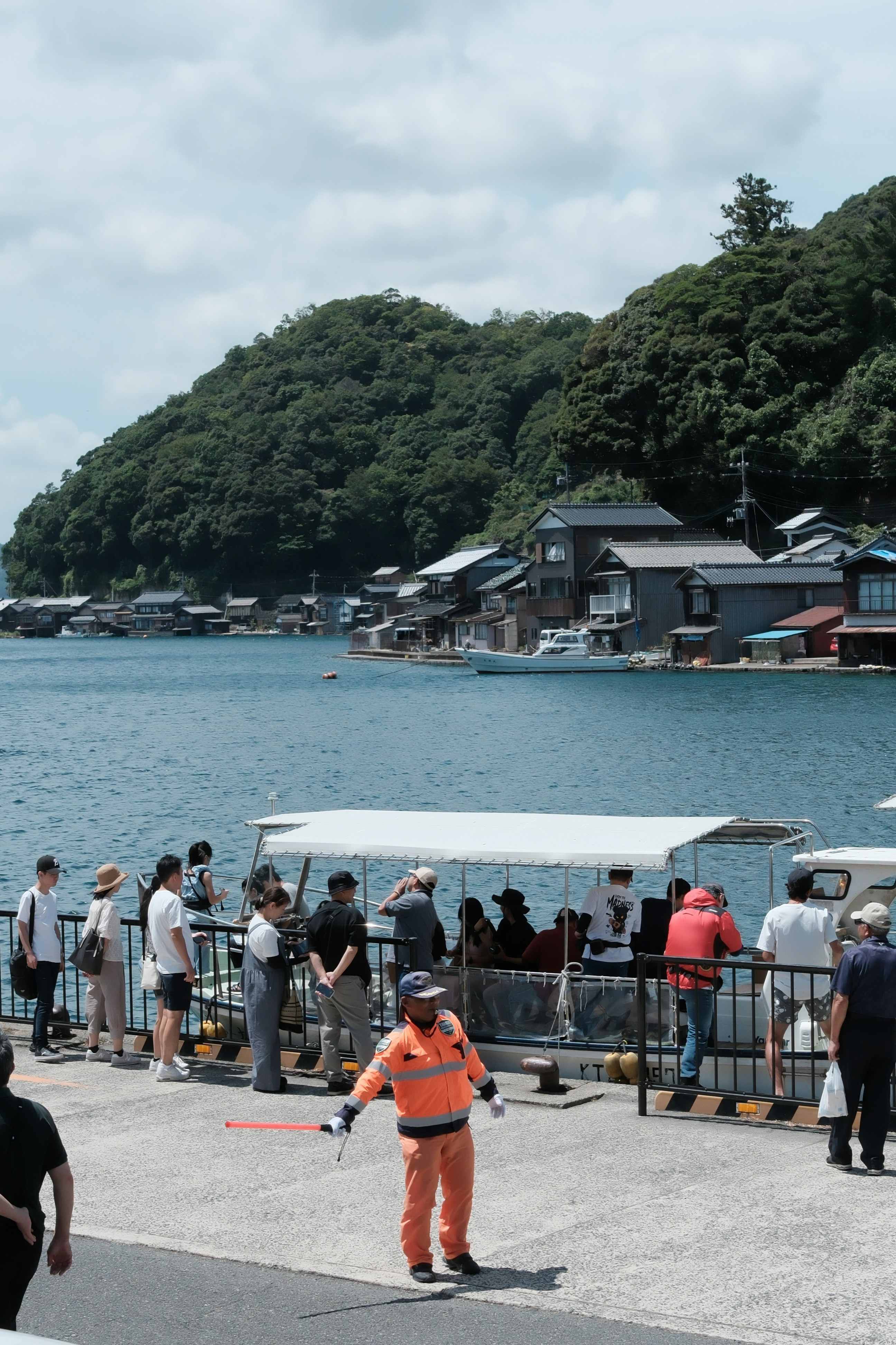 Colorful waterfront village and a guidance crew along a harbor with a covered boat dock and people by the railing.