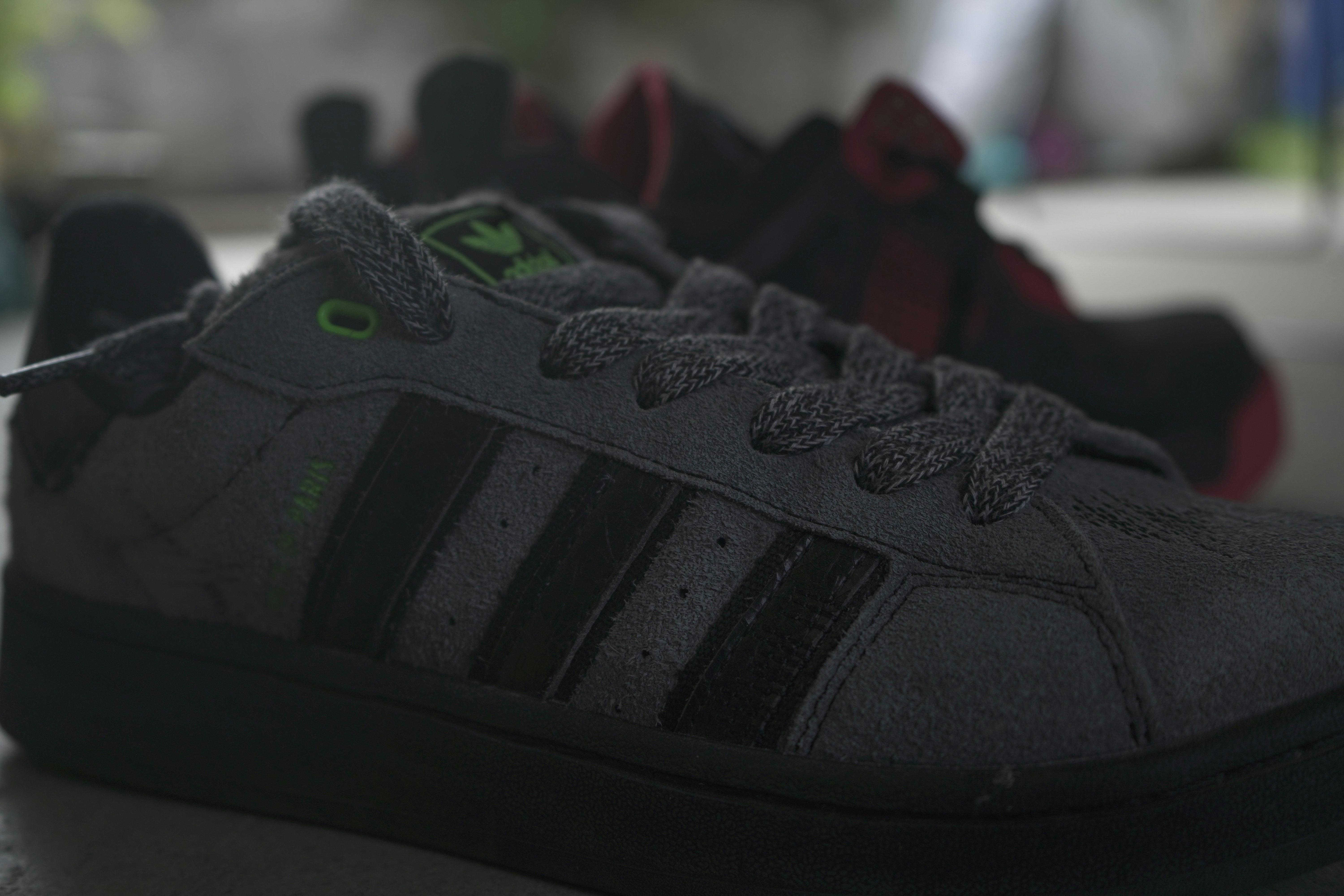 Low-angle close-up of a dark sneaker with subtle stripes in a dimly lit scene