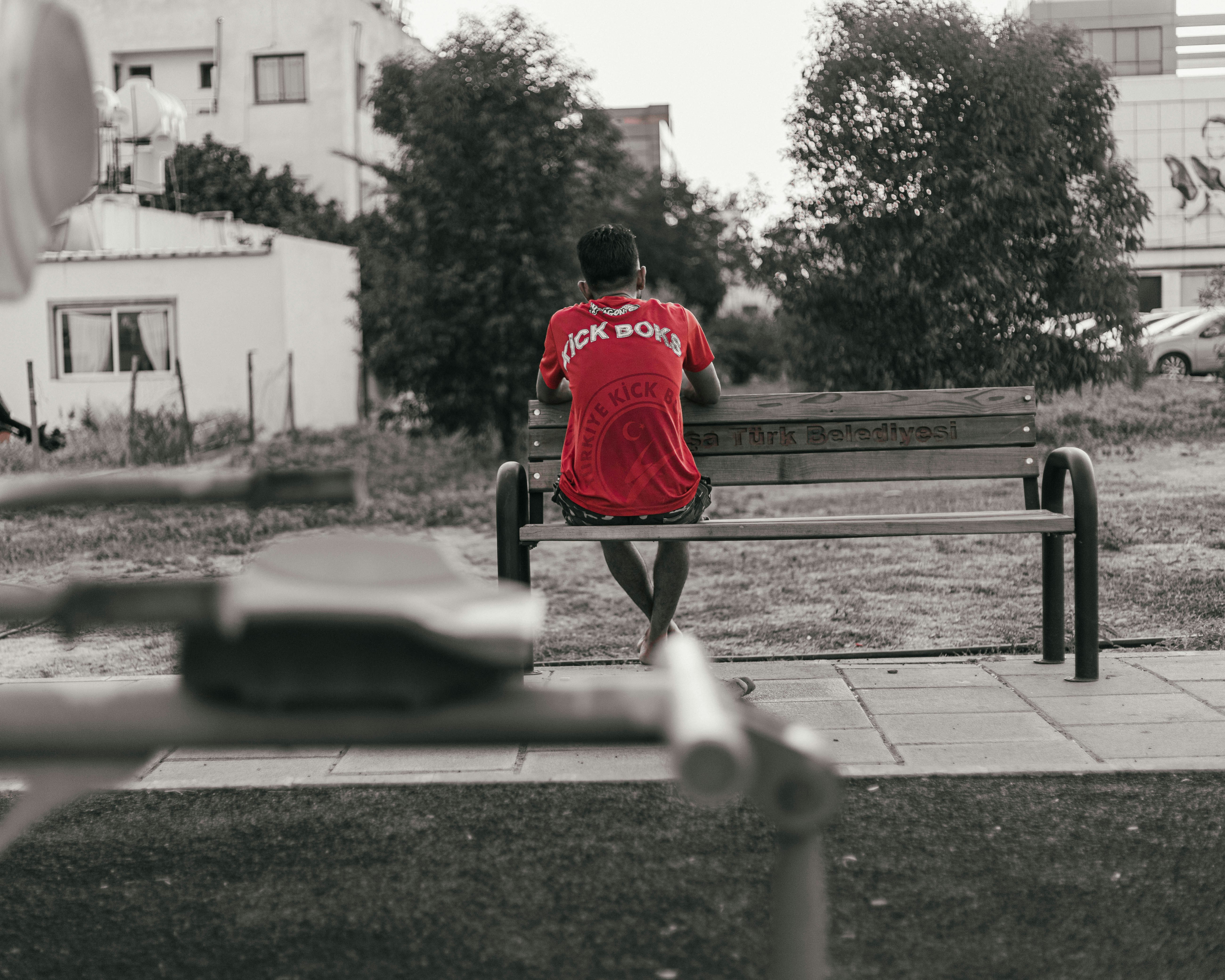 Red Jersey in Quiet Park: A Lone Moment on a Wooden Bench