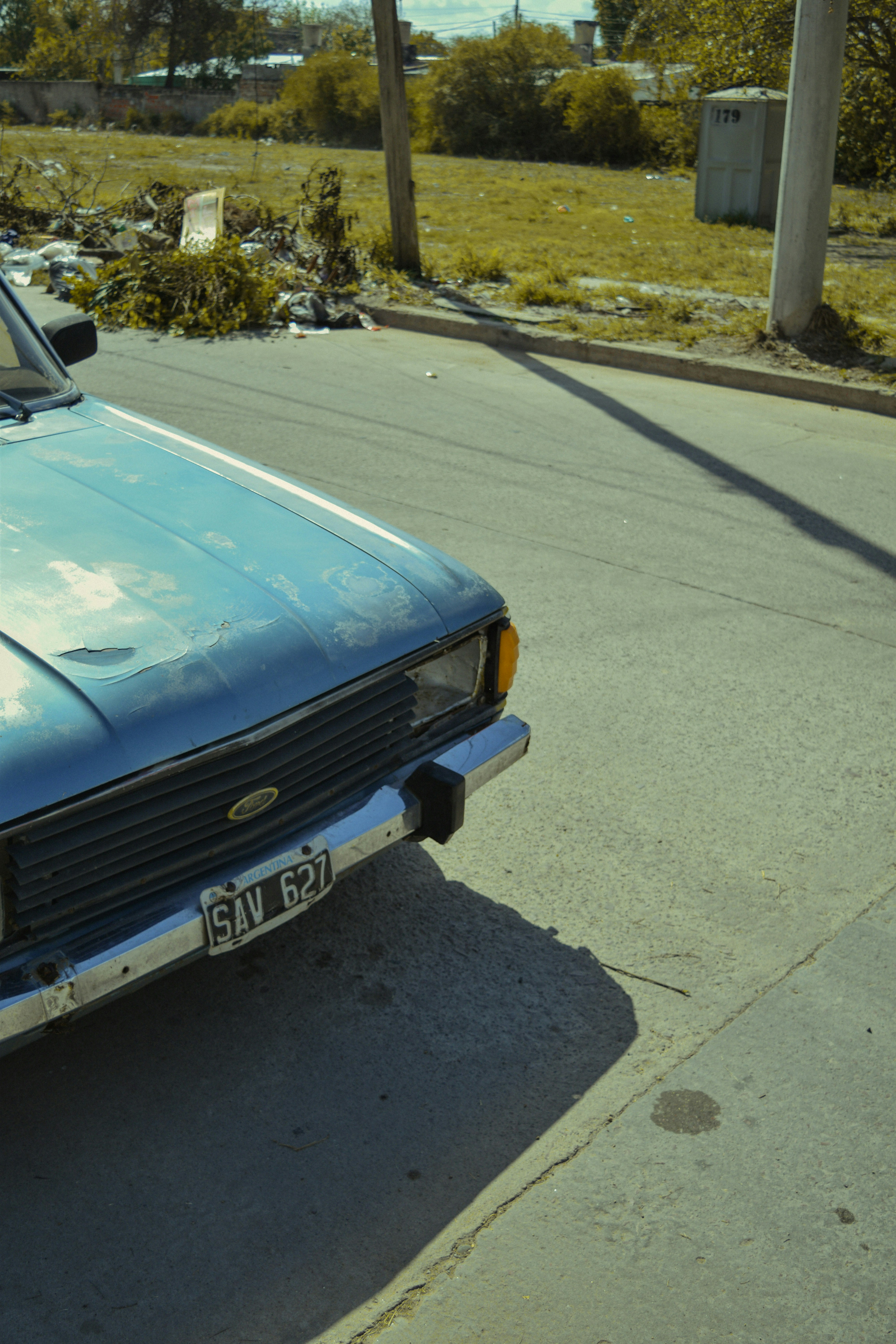 An old blue car at the curb under a sunlit suburban street