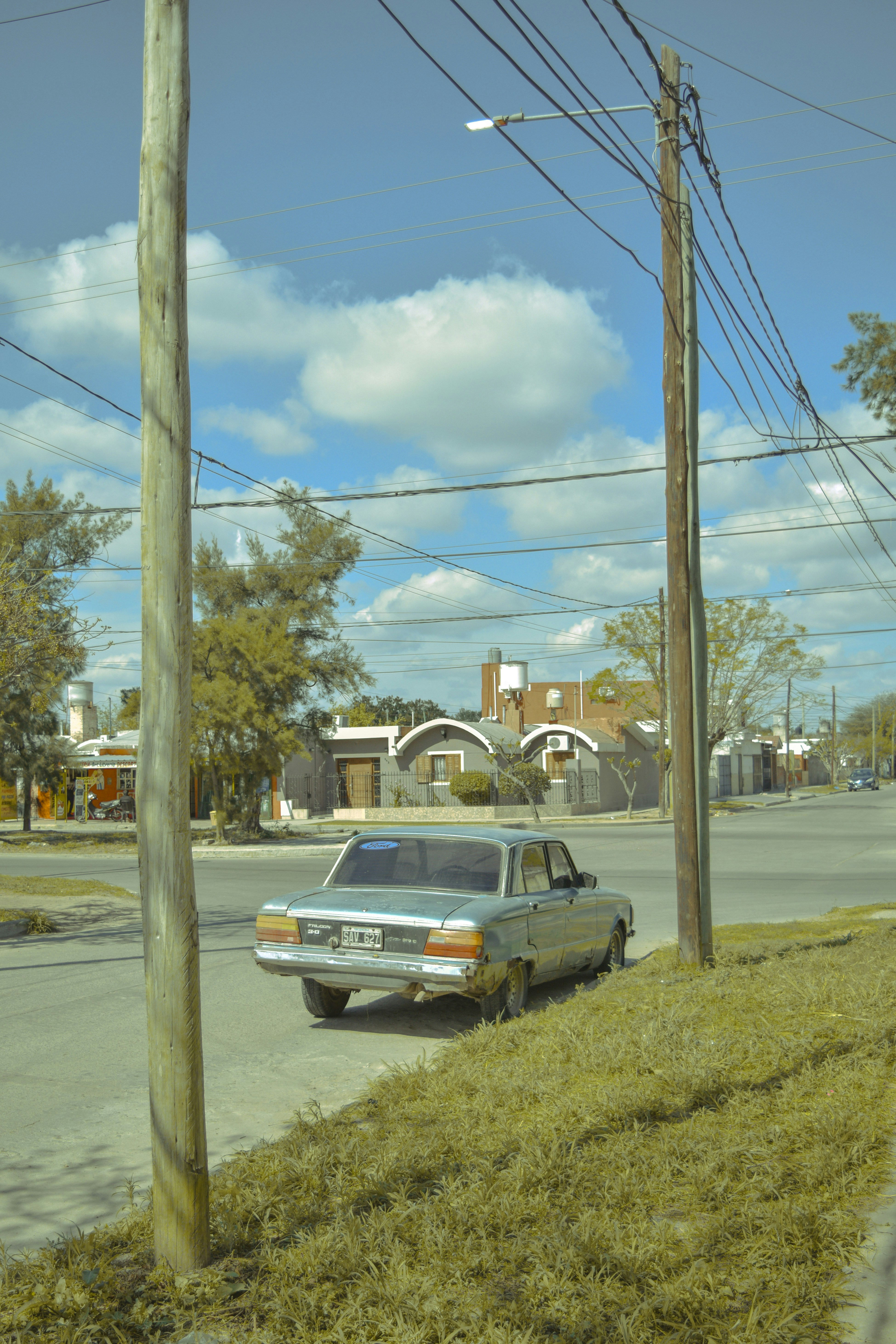 Rusty sedan on a sunlit street framed by utility poles