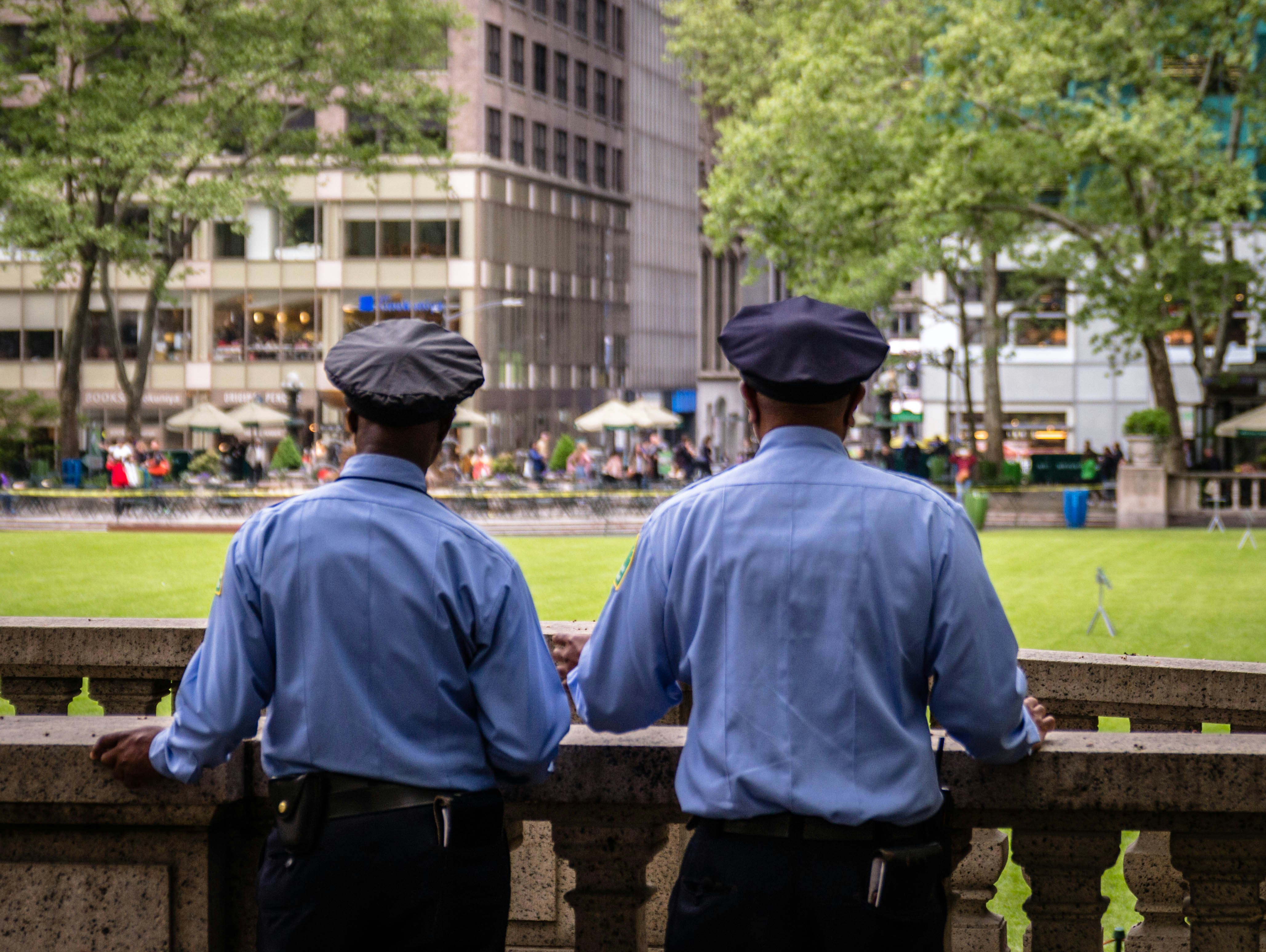 Two uniformed security guards sit overlooking a busy green space in New York City. A candid urban photograph capturing everyday city life, public spaces, work, and the distinctive atmosphere of Manhattan.