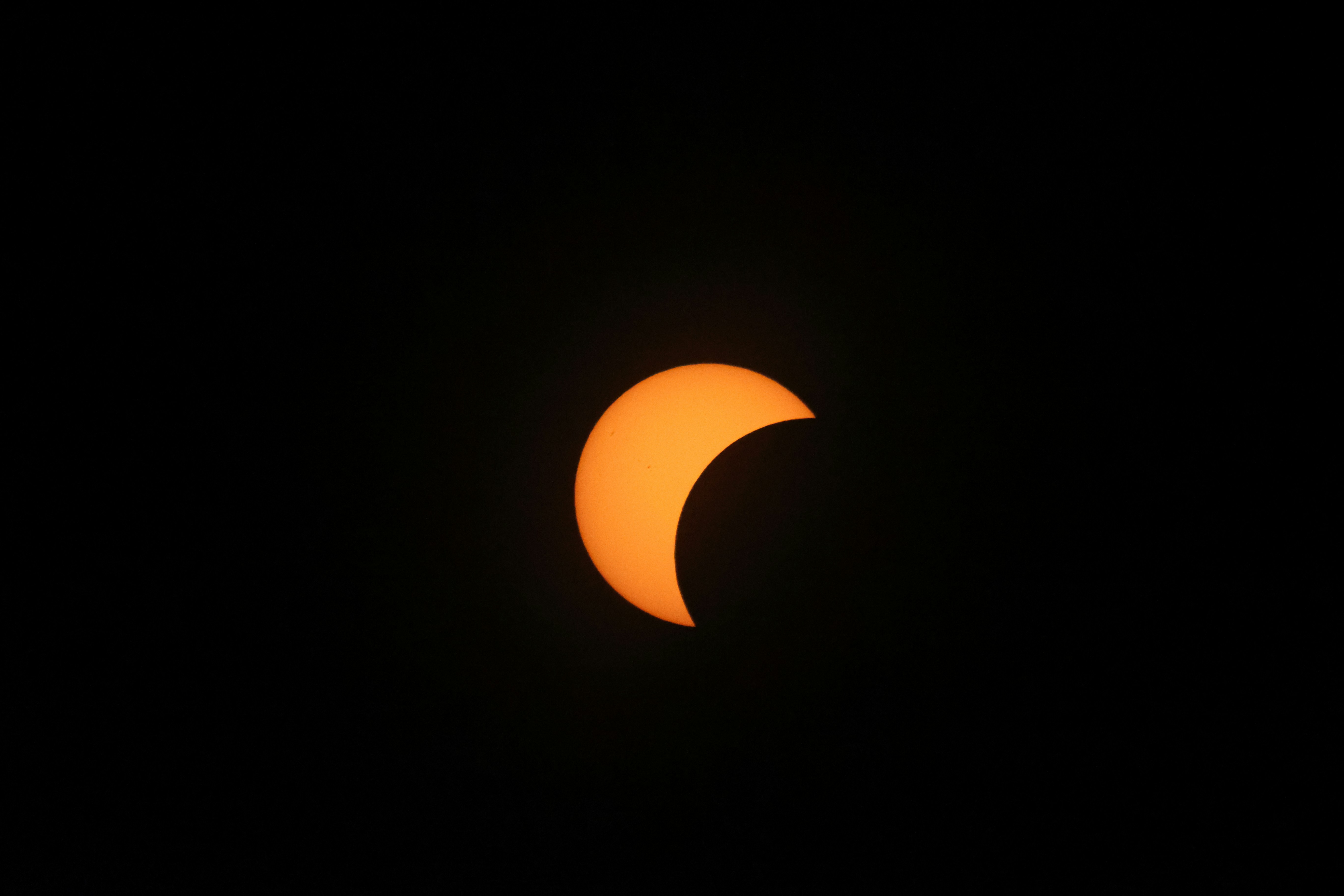 A partial solar eclipse showing a glowing orange crescent against a black sky