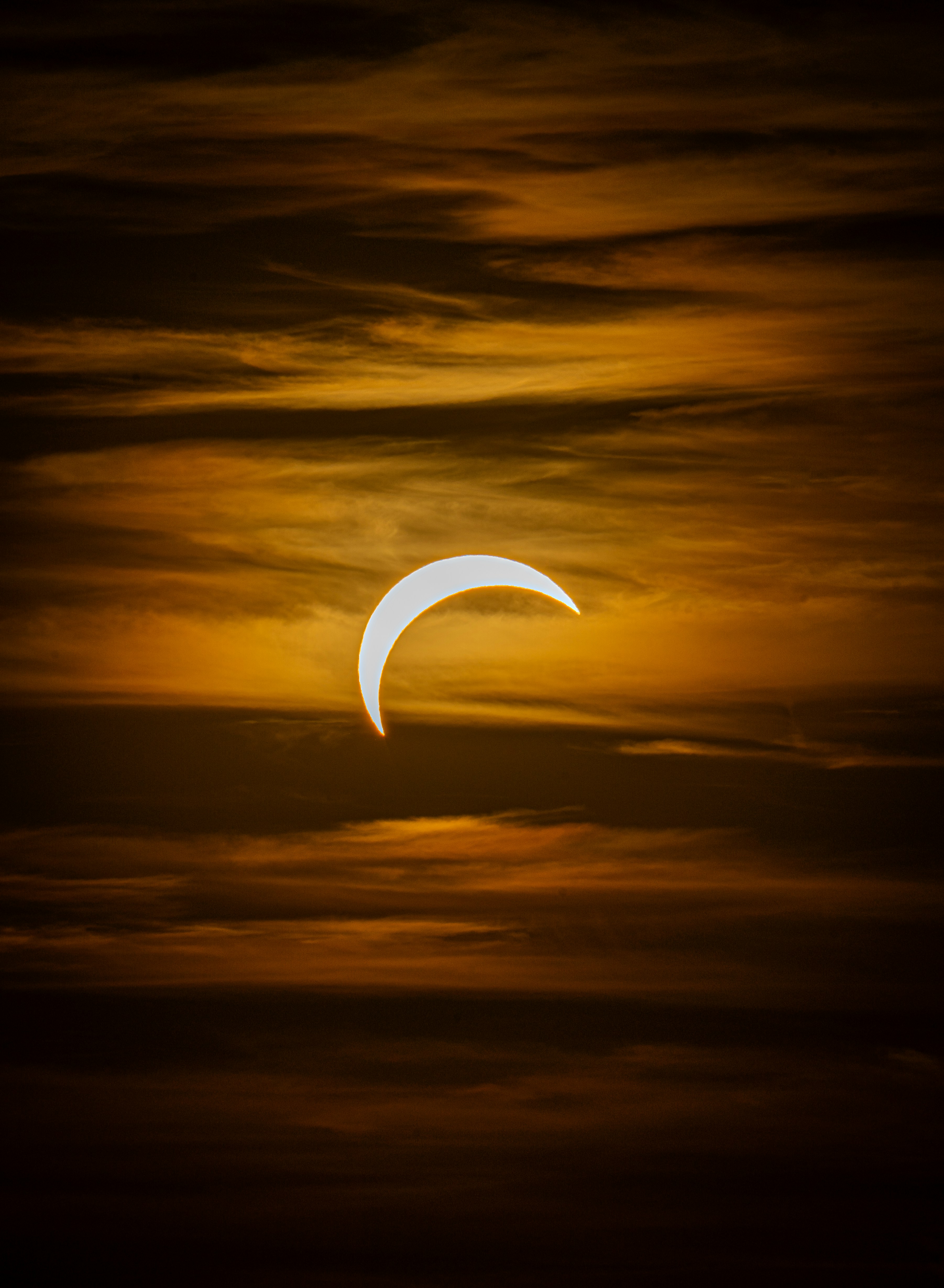 A crescent sun partially eclipsed by the moon behind dark orange clouds