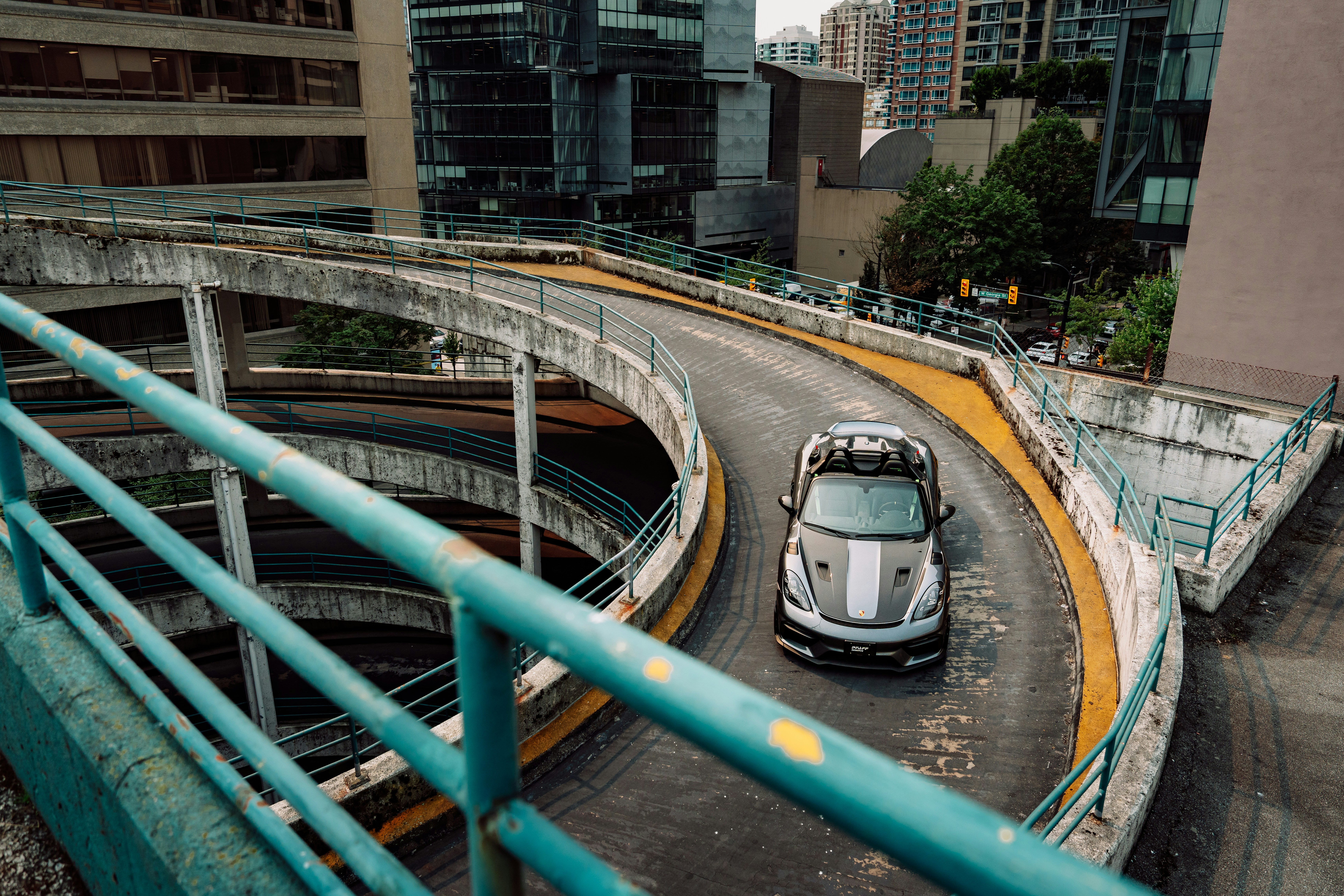 Coiled Ascent: A Silver Car Navigates a Circular Ramp Above Urban Tiles
