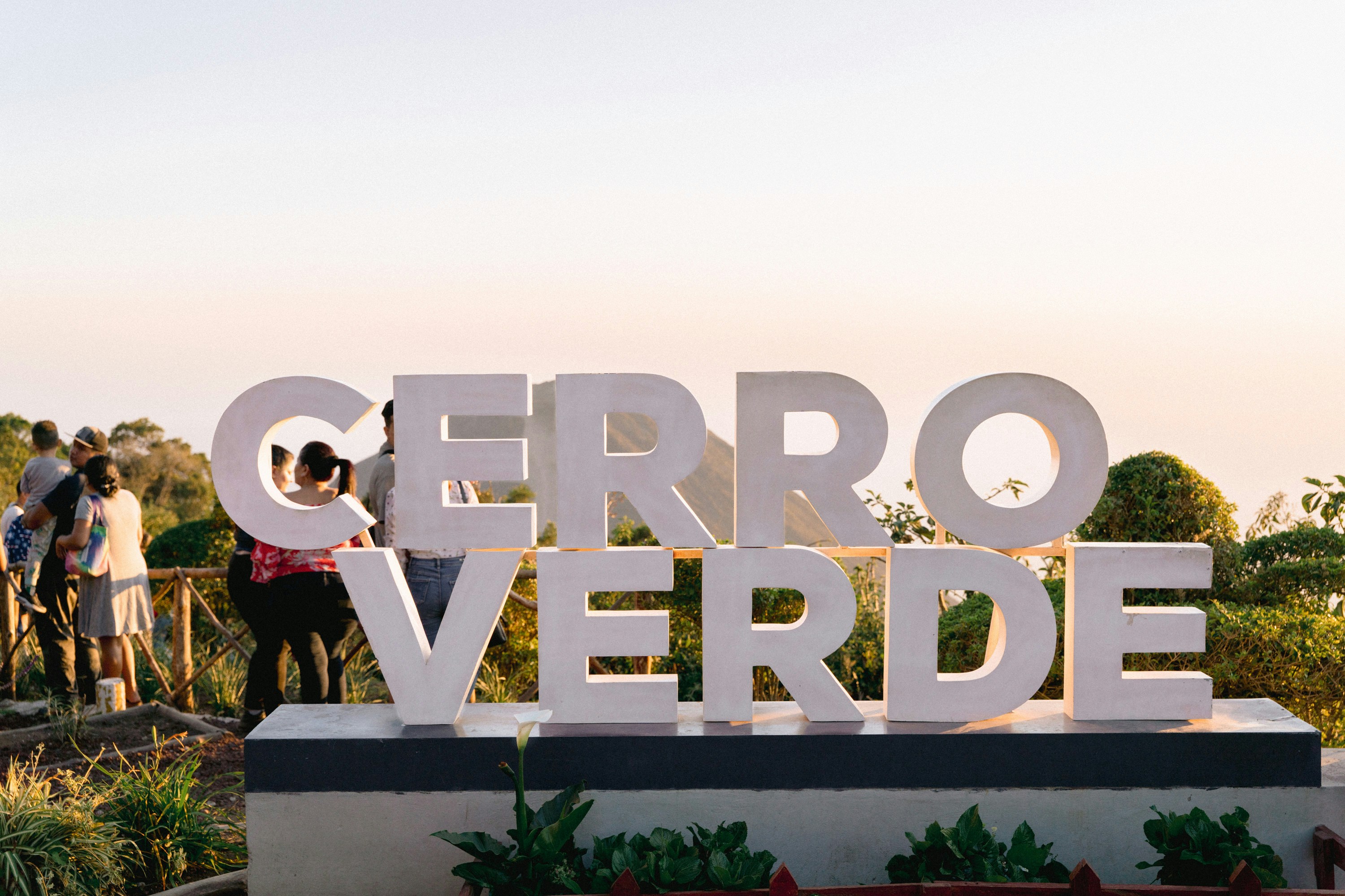 Bold CERRO VERDE sign sits atop a platform with warm sunset lighting; a group of people foreground-left adds depth and scale.