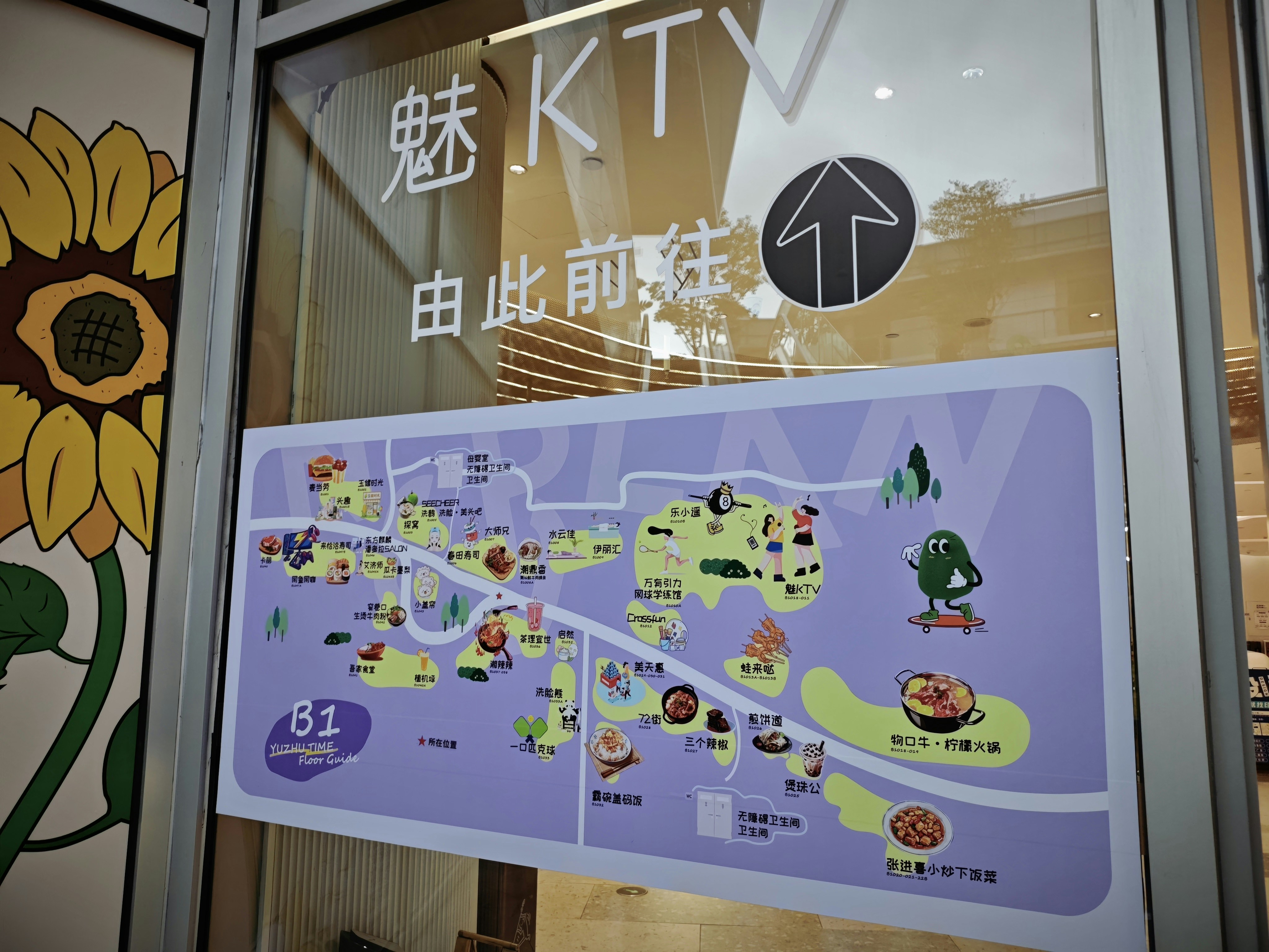 Colorful illustrated map displayed behind glass at a storefront, with white Chinese text and a sunflower mural on the left; signage and arrow graphic visible above the map.
